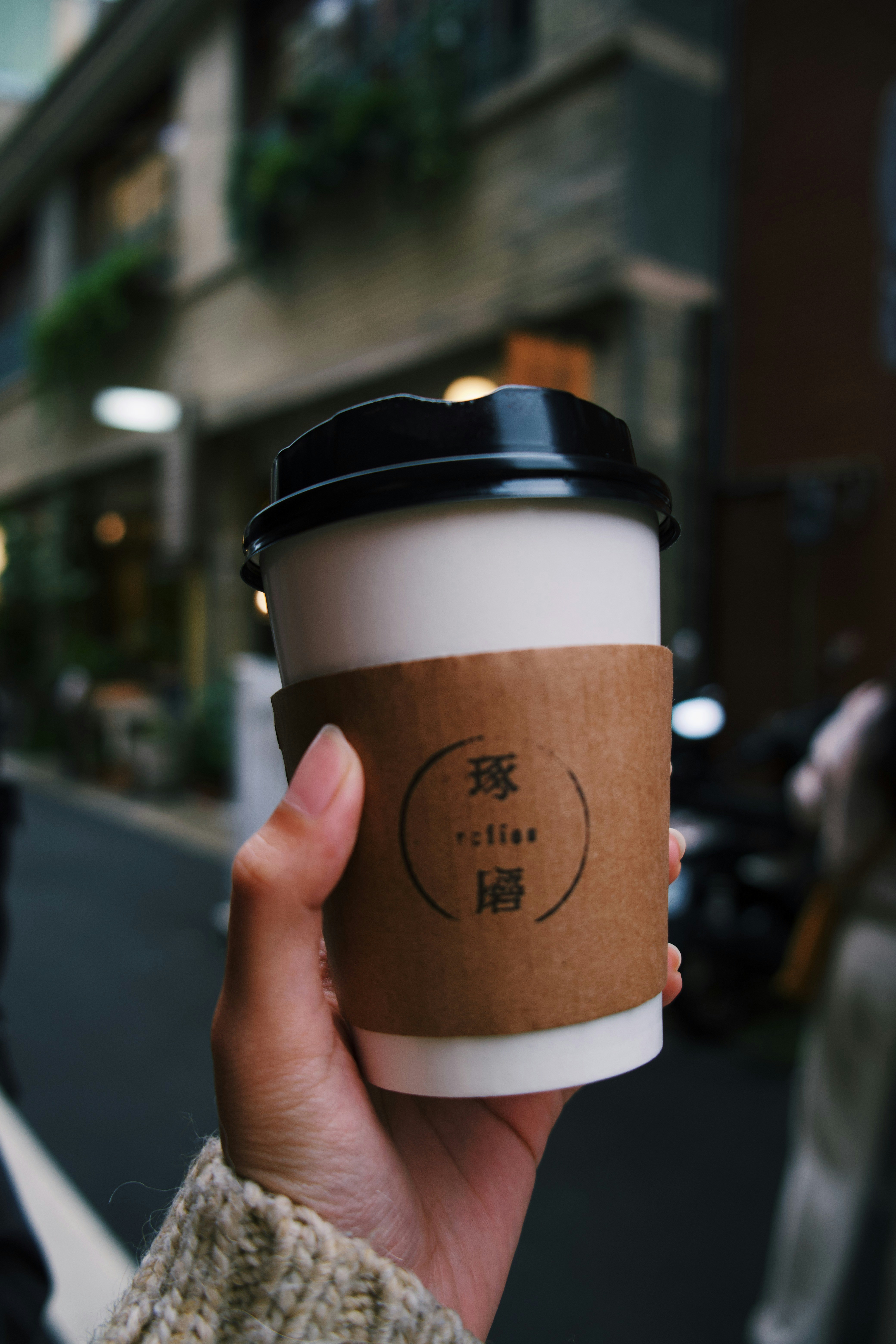 Urban Focus: A Hand-Clasped Coffee Cup Against a Soft Street Blur