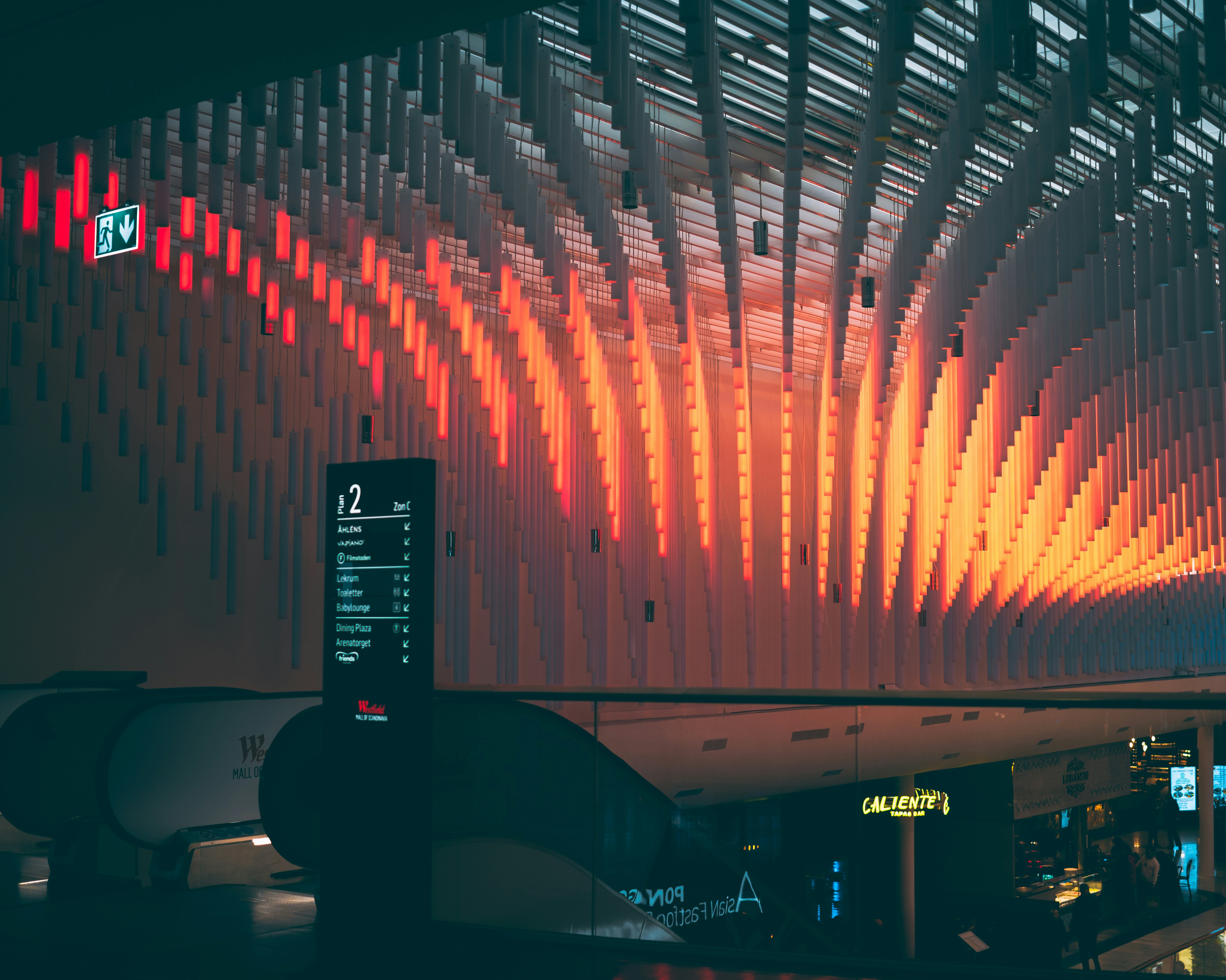 Dynamic ceiling installation with red and white lights casting a wave-like pattern in a modern architectural space.