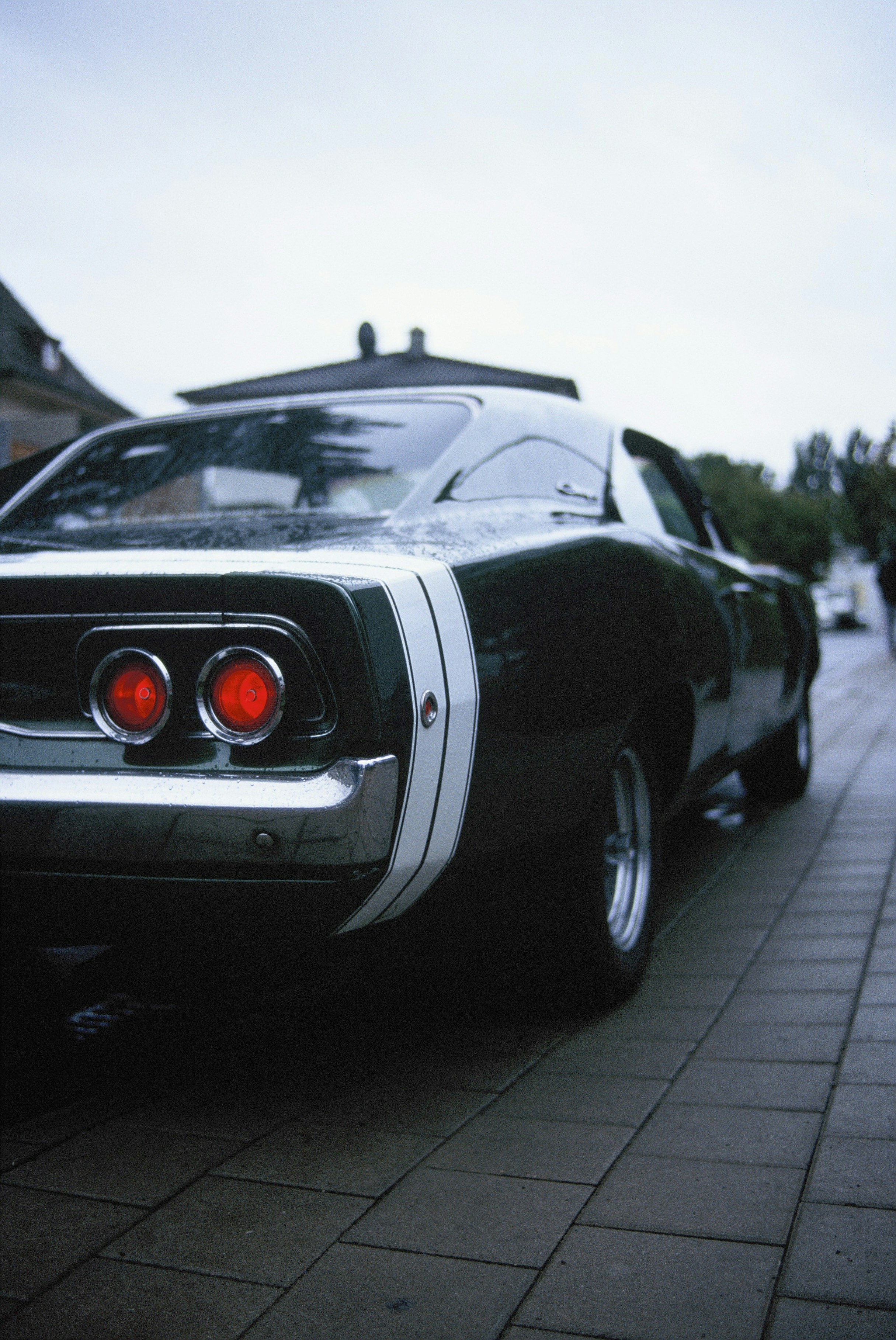 Twin Red Halos on a Quiet Street: A Classic Muscle Car Resting Under Cloudy Light