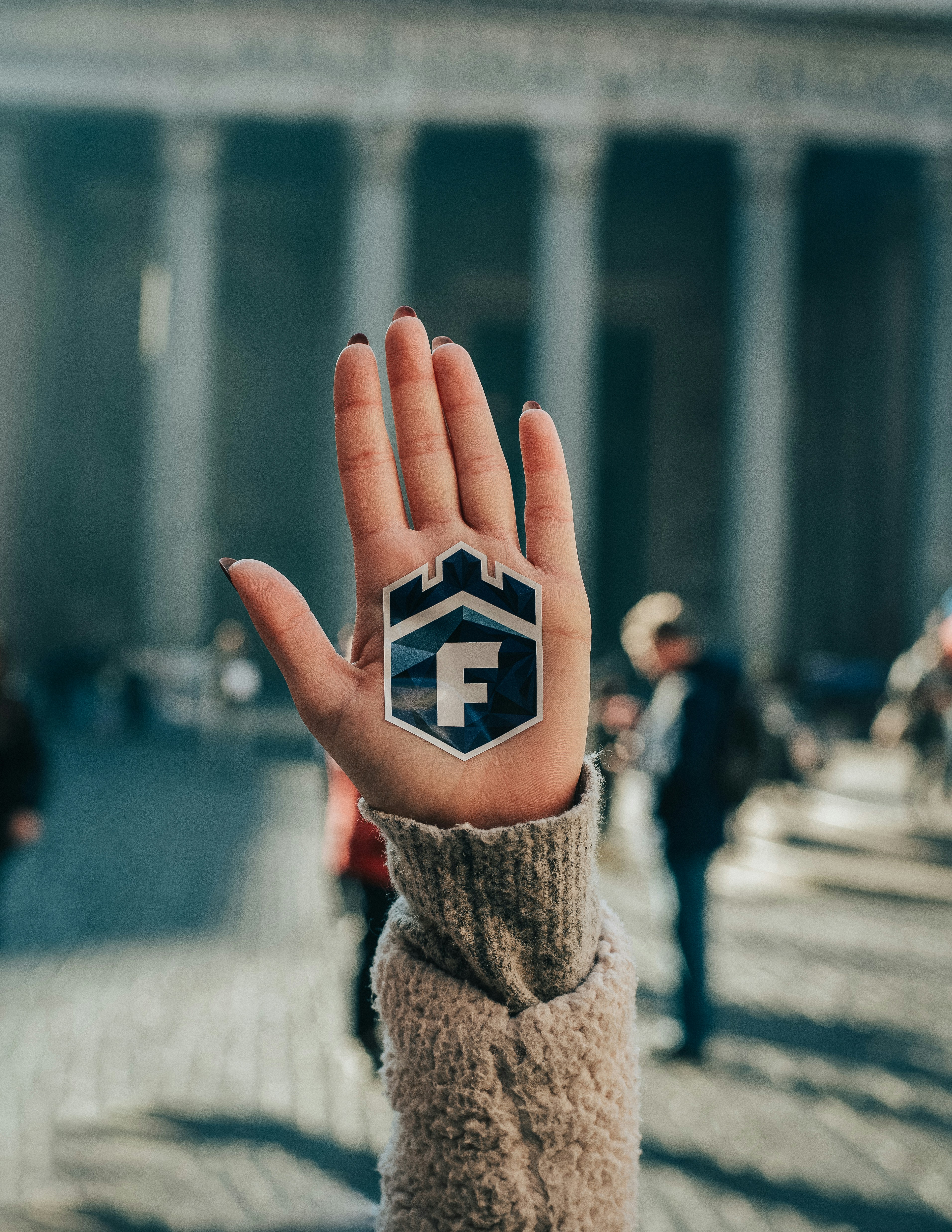 Handheld Symbol: A Raised Palm with a Shield Logo Before a Classical Facade
