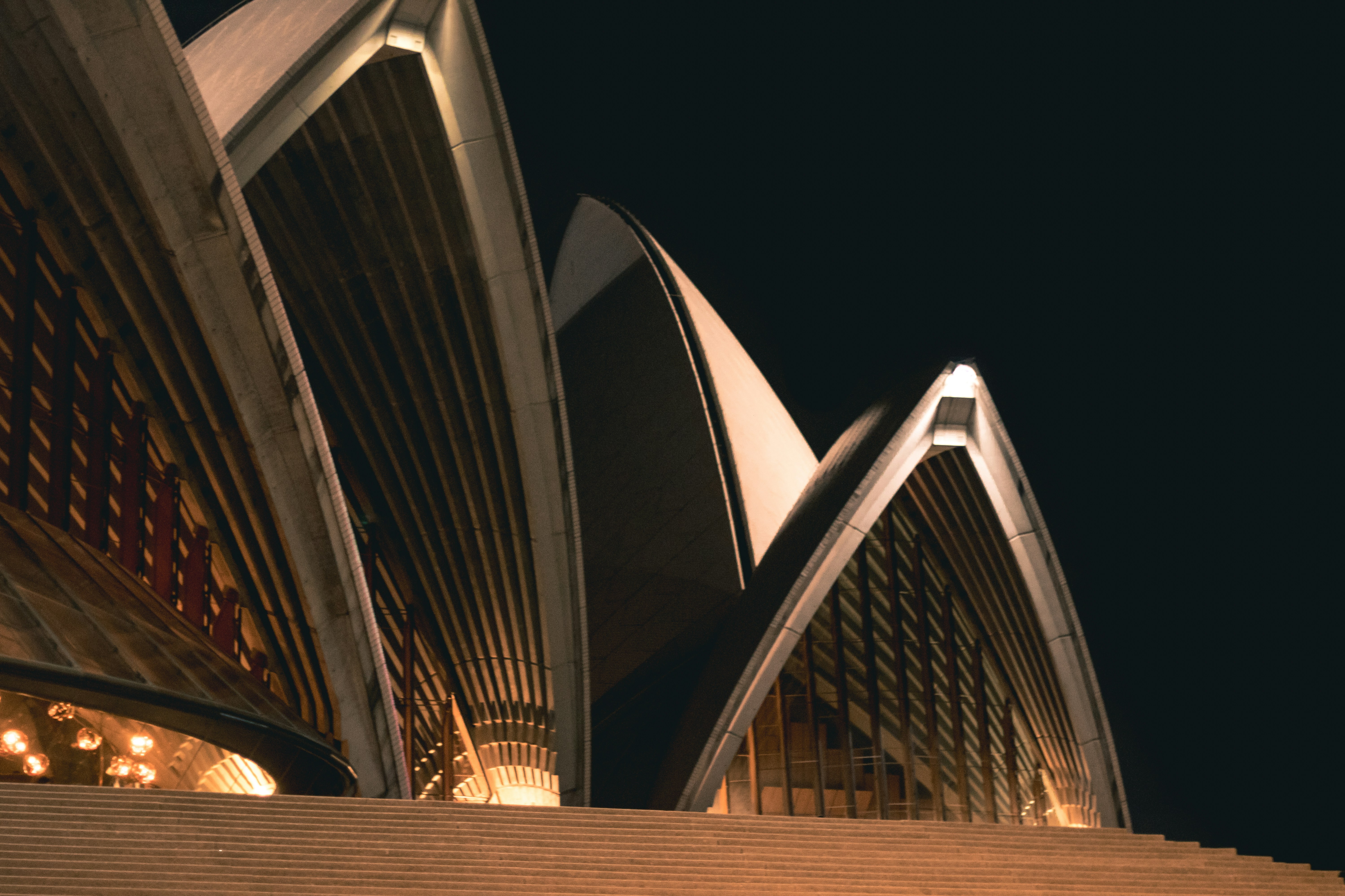 The iconic sails of the Sydney Opera House illuminated against a dark sky, showcasing modern architectural design. The interplay of light and shadow enhances the structure's unique form.