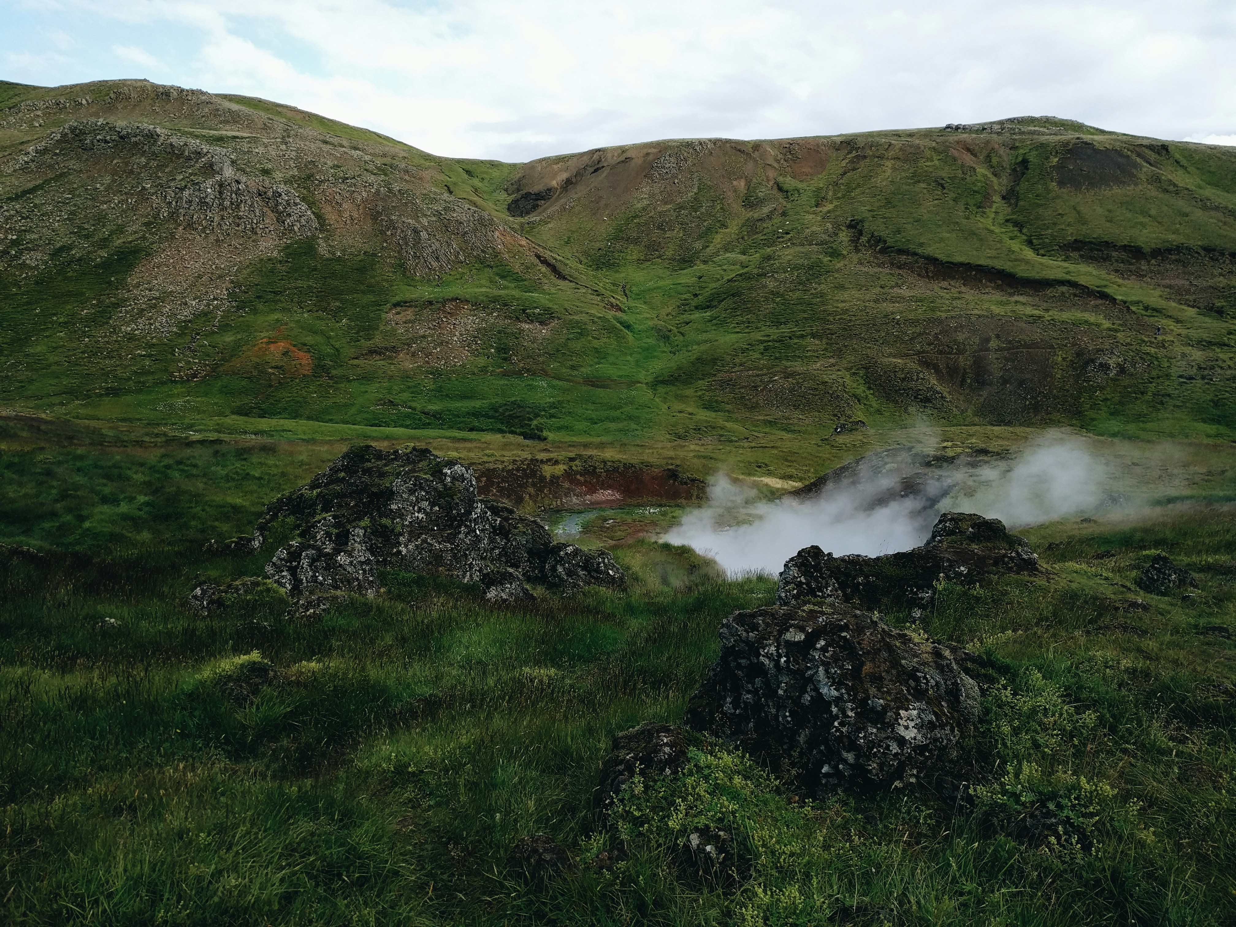 Rolling moorland with green slopes and rocky outcrops, punctuated by rising mist near the center. This landscape emphasizes moorland texture and atmospheric depth.