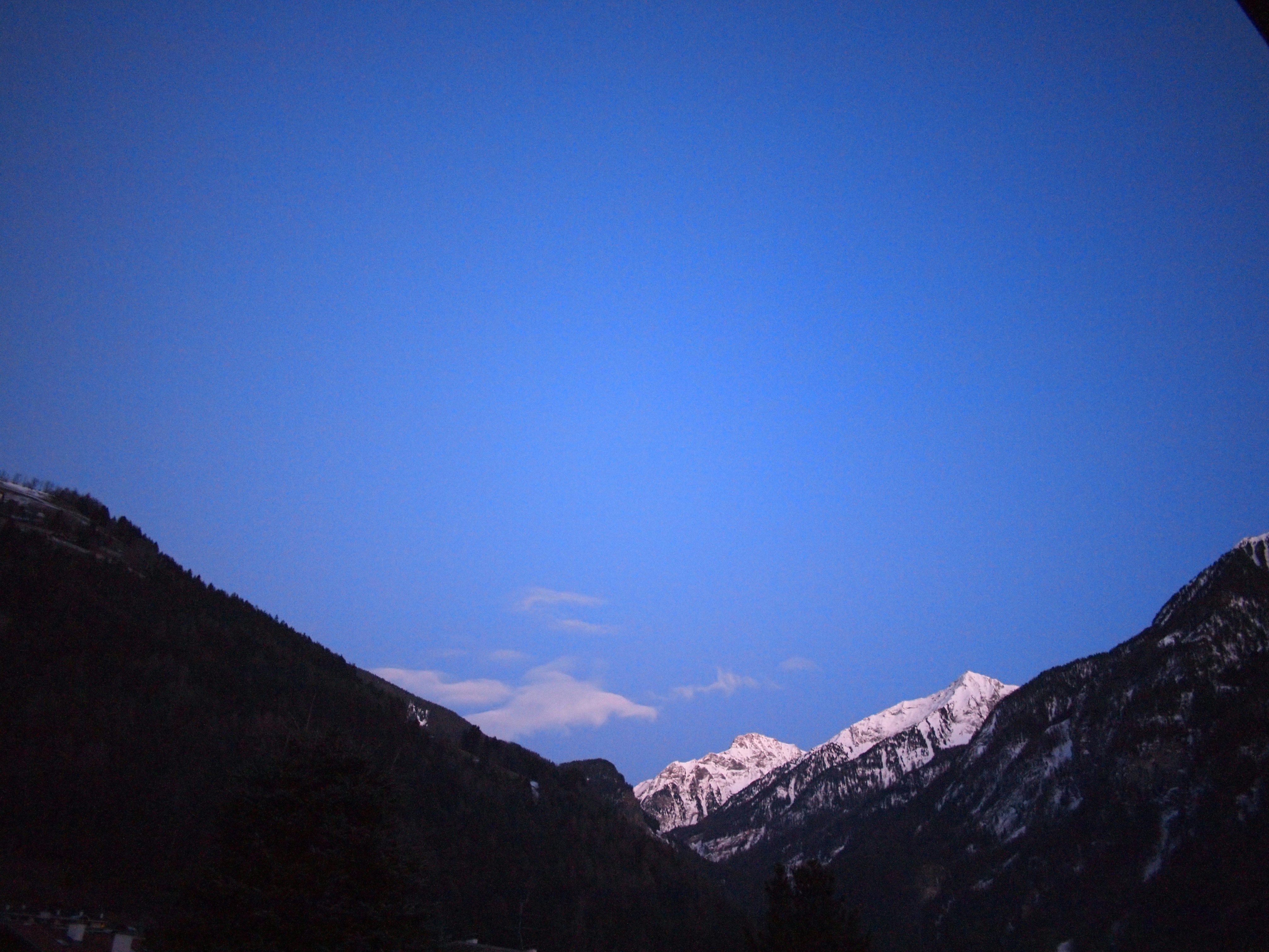 Snow-capped mountains silhouetted against a deep blue twilight sky.