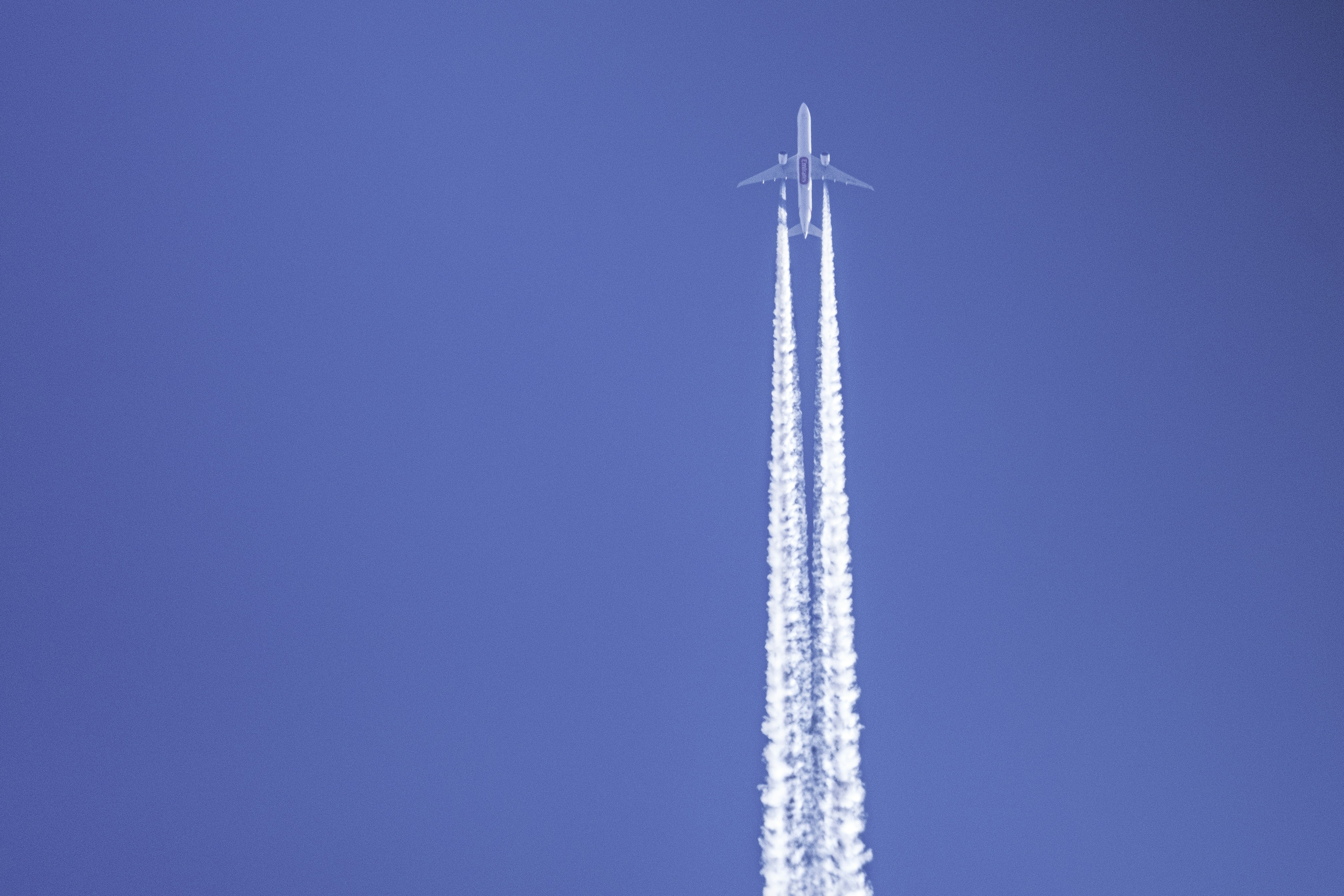 Airplane soaring through a clear blue sky, leaving parallel contrails.