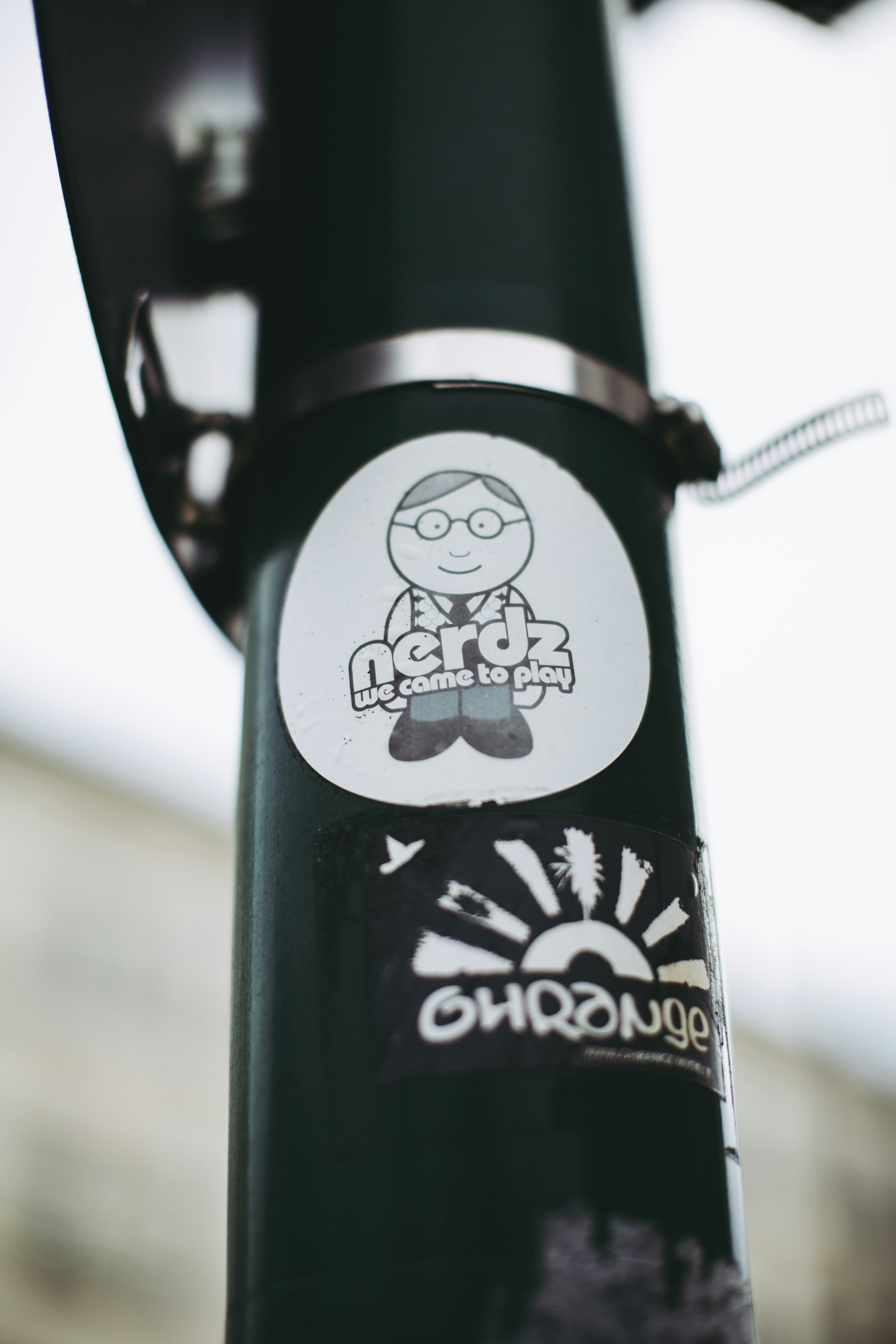 Streetlight pole adorned with a cartoon sticker reading 'nerdz we come to play.'