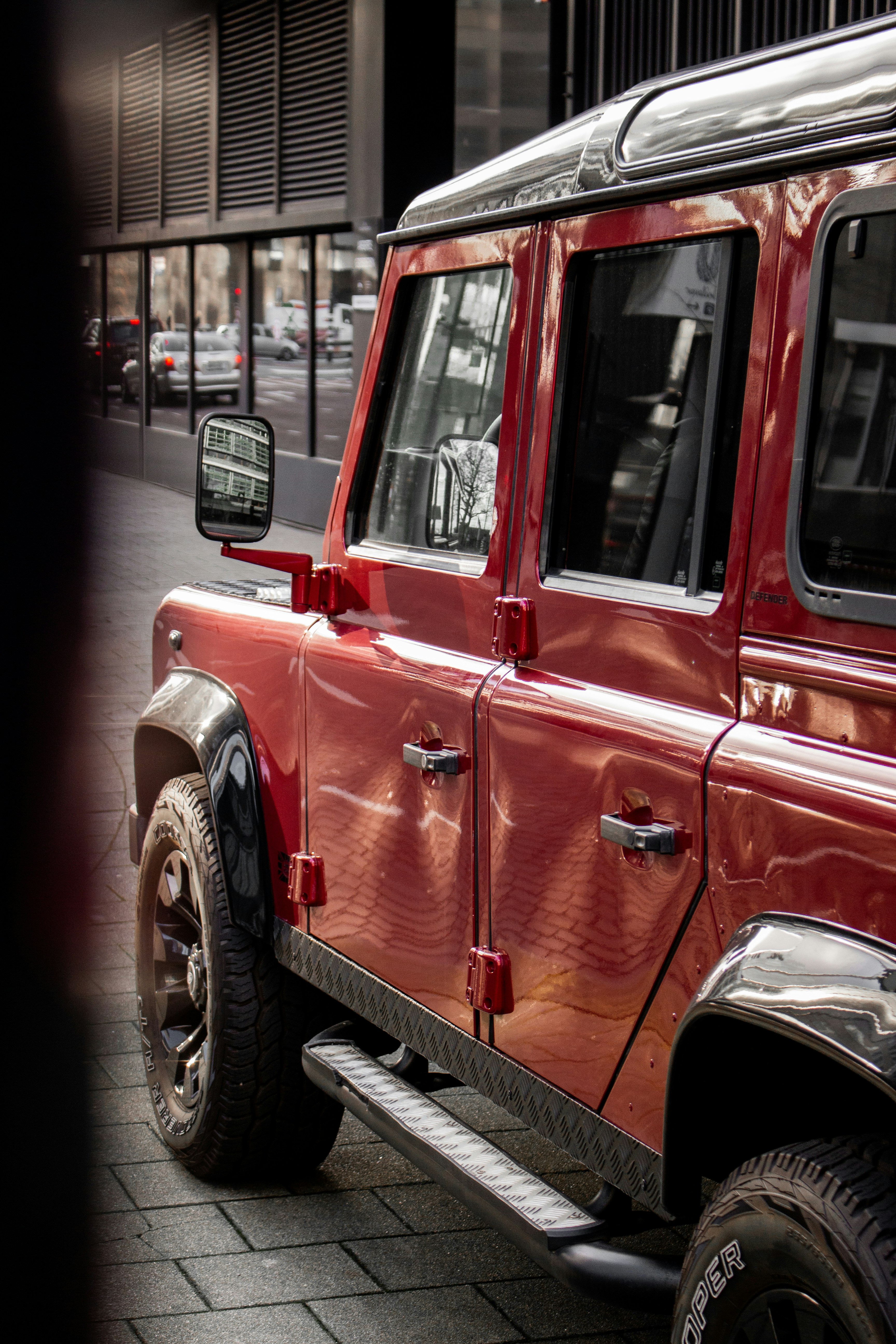 Crimson Behemoth: A Red Jeep Anchored in Urban Glass