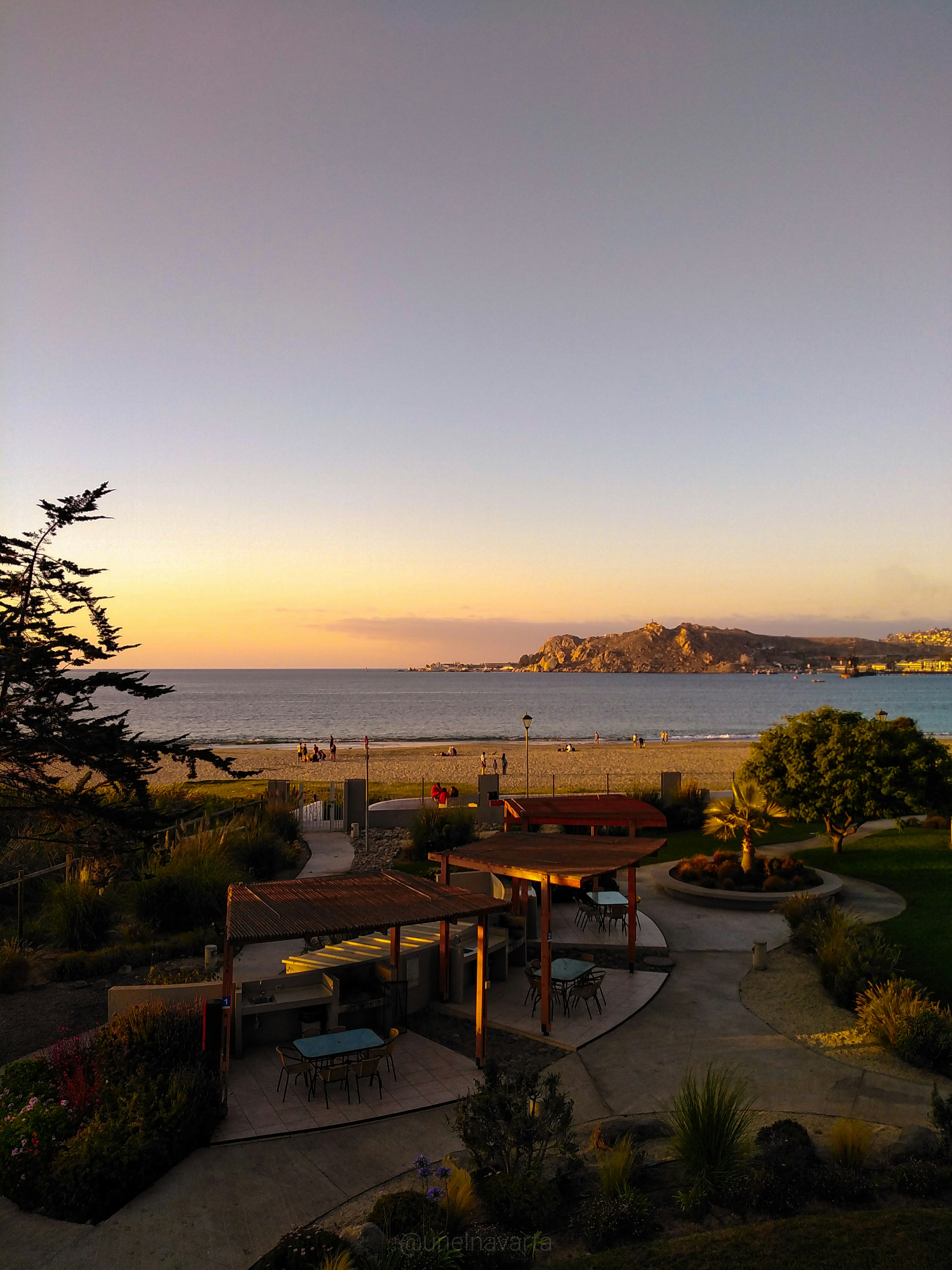 Sunset view of La Herradura beach with a tranquil seaside park and distant hills under a golden sky.