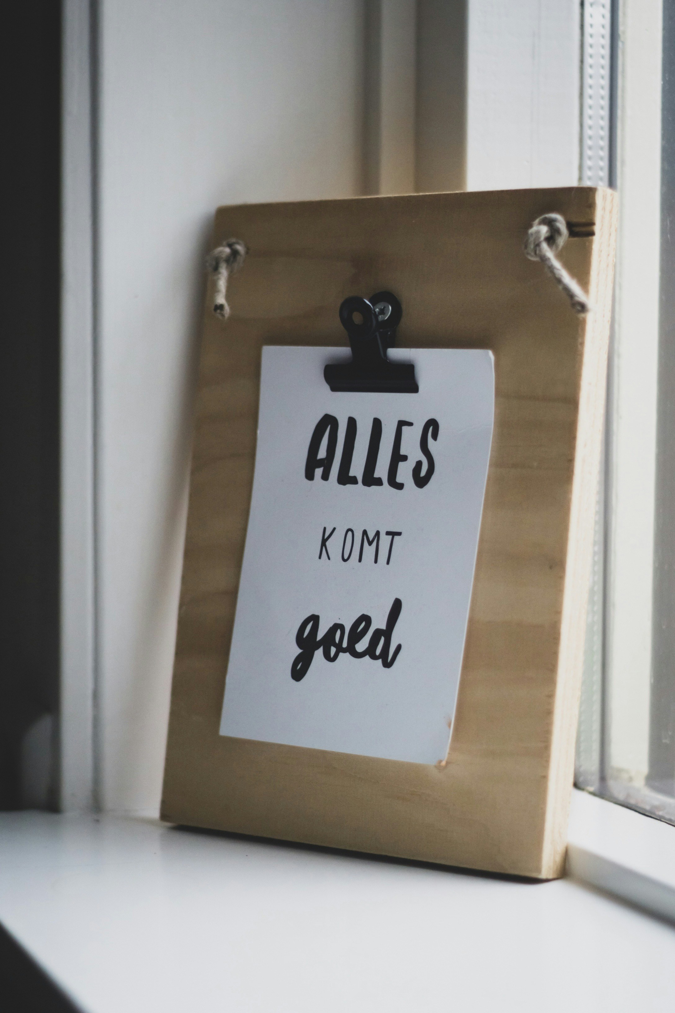 Wooden board with a clip and Dutch sign that says: Everything’s going to be allright.