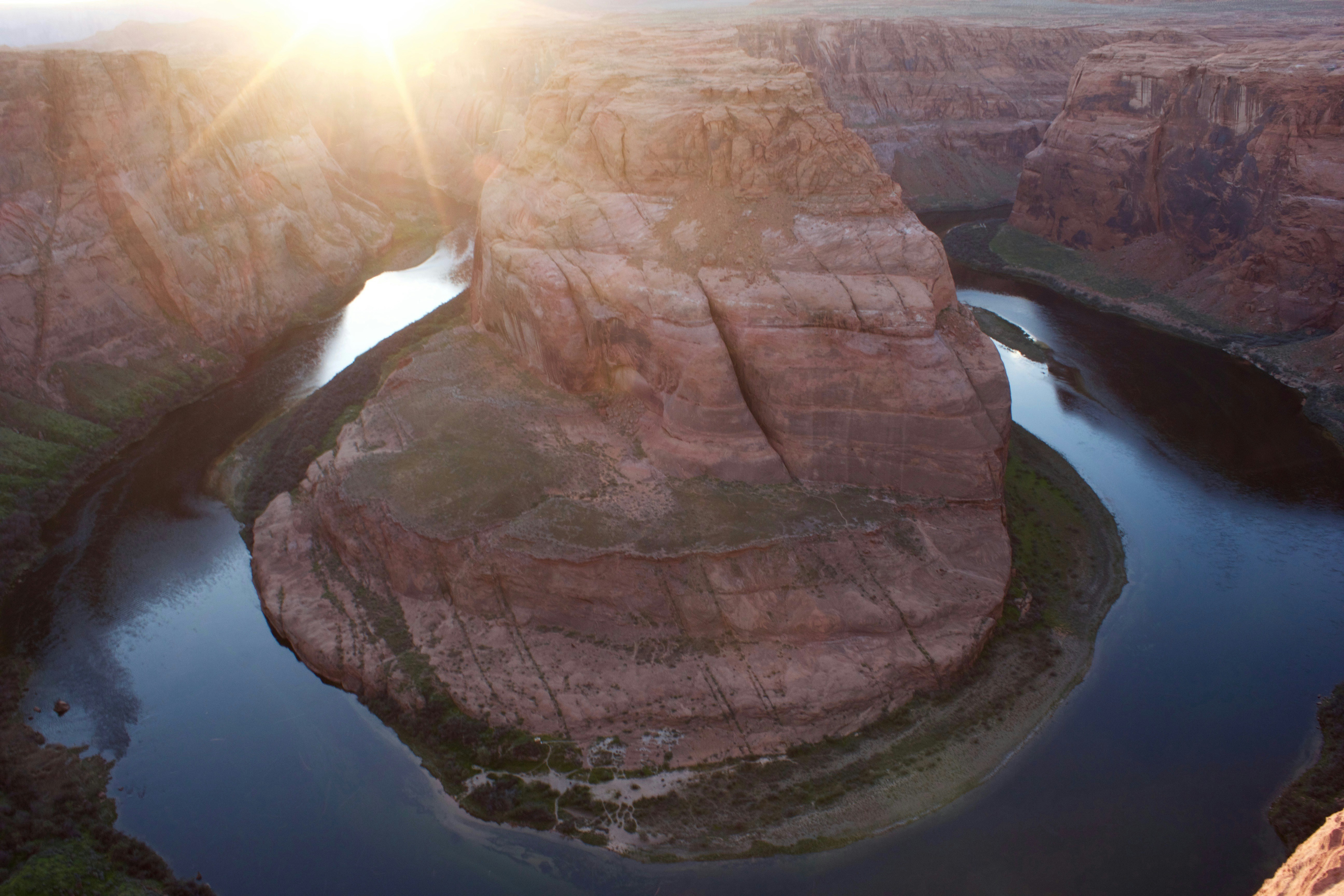 Curved river flowing around a massive sandstone formation at Horseshoe Bend, illuminated by the warm glow of the setting sun.