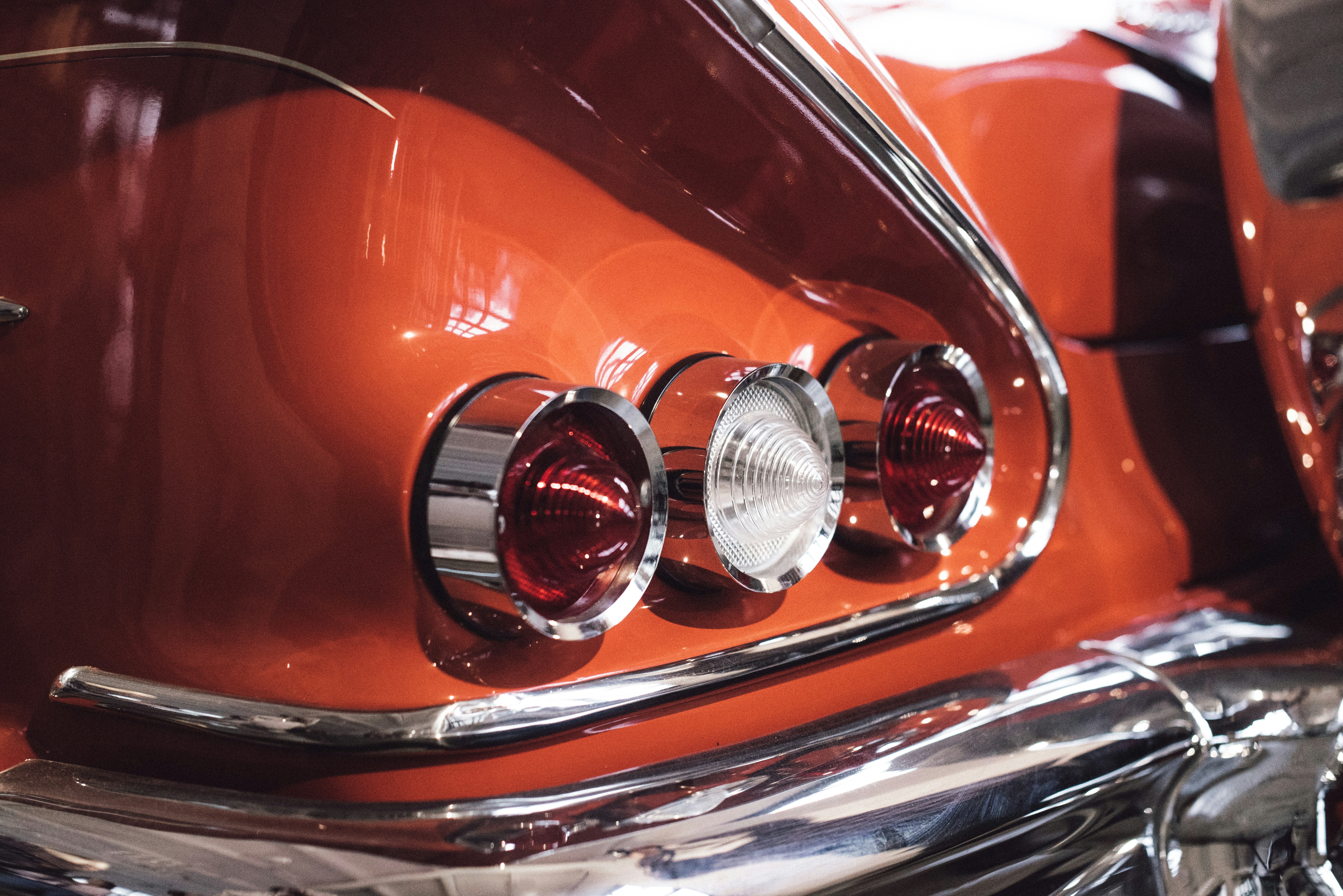 Three Chrome-Rimmed Tail Lights on a Velvet Orange Classic Car