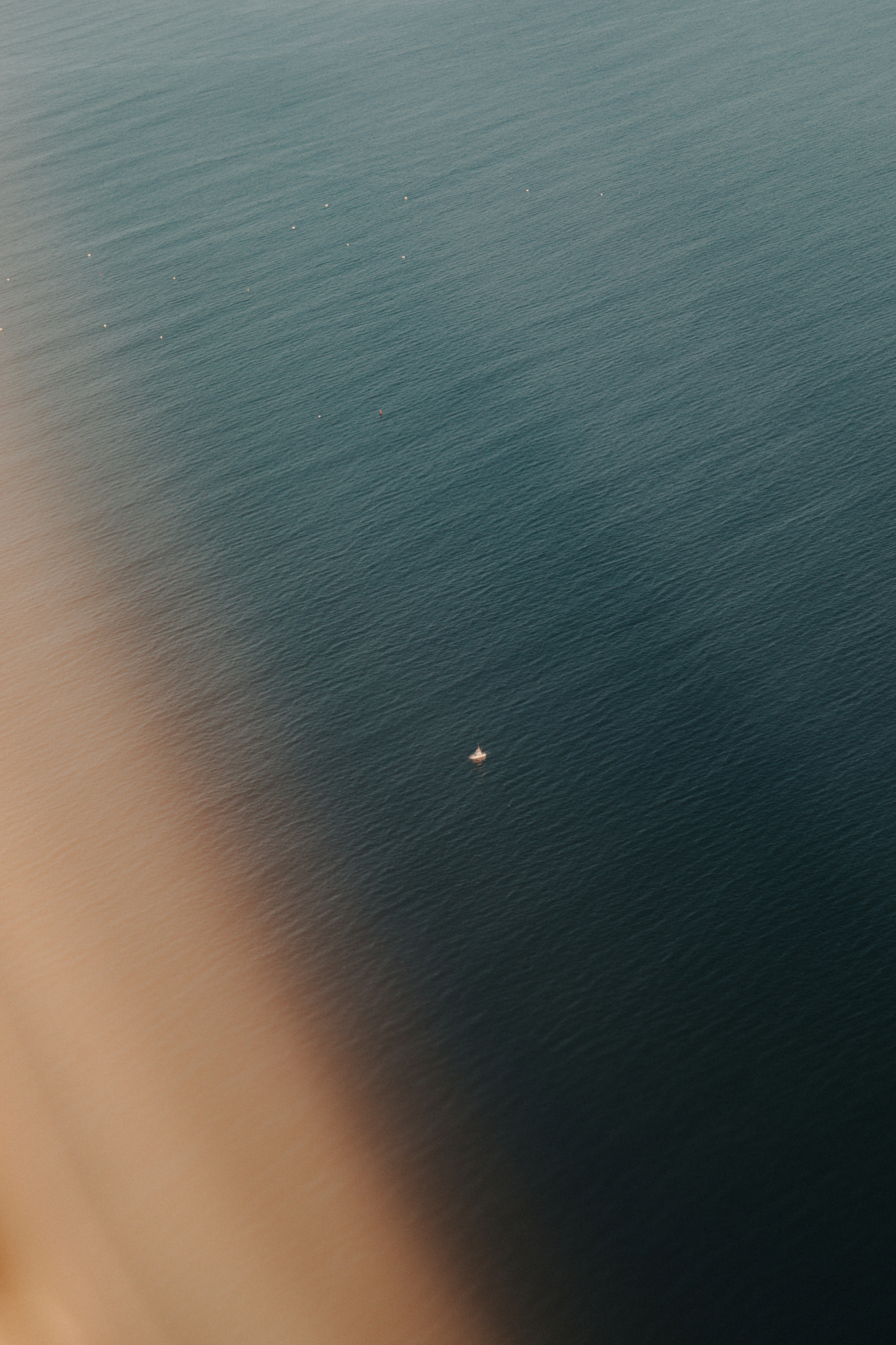 A solitary boat drifts across a serene expanse of deep blue ocean, bordered by a soft sandy shoreline.