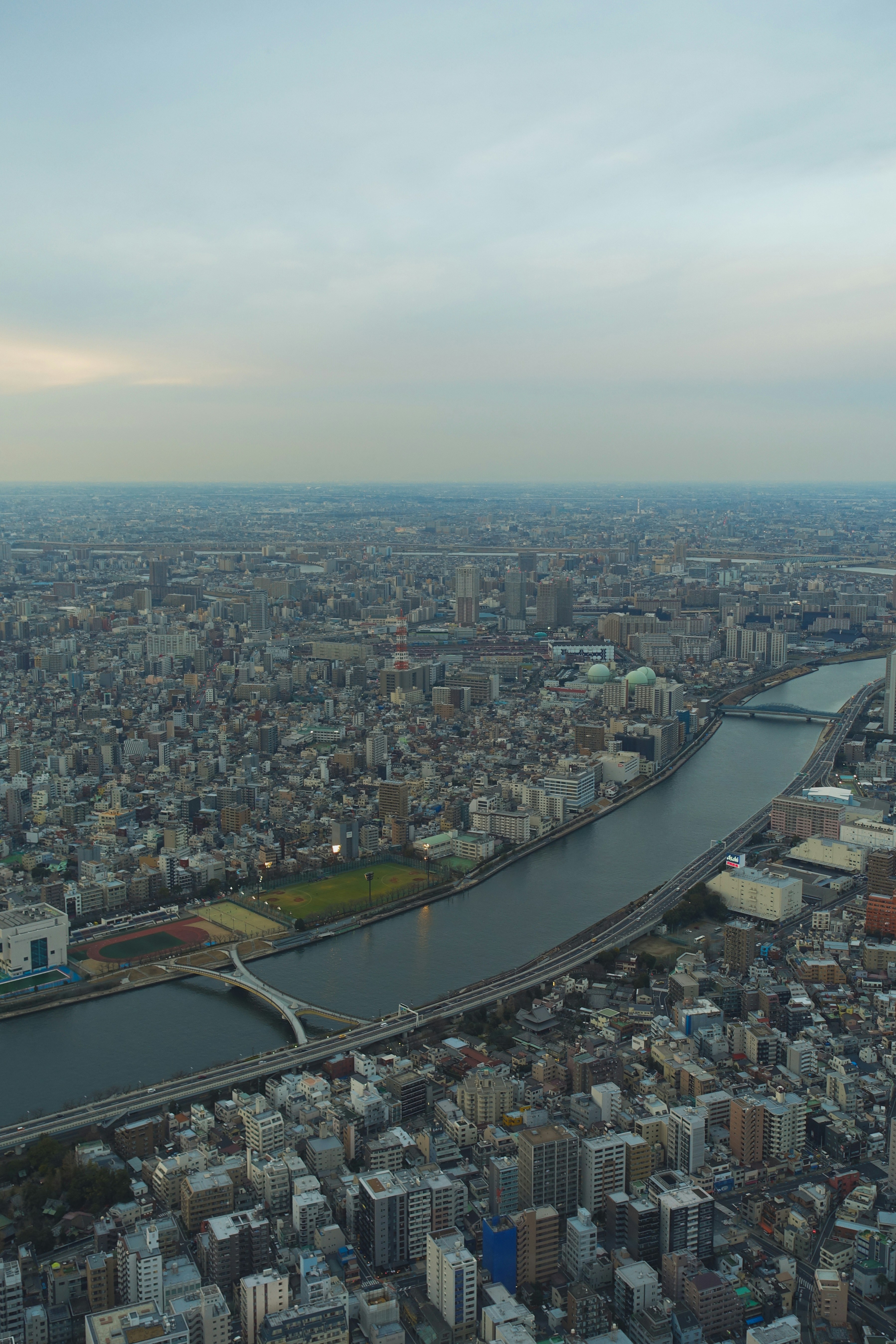 Aerial view of a sprawling urban landscape with a river winding through the city, showcasing the intricate layout of buildings and green spaces.