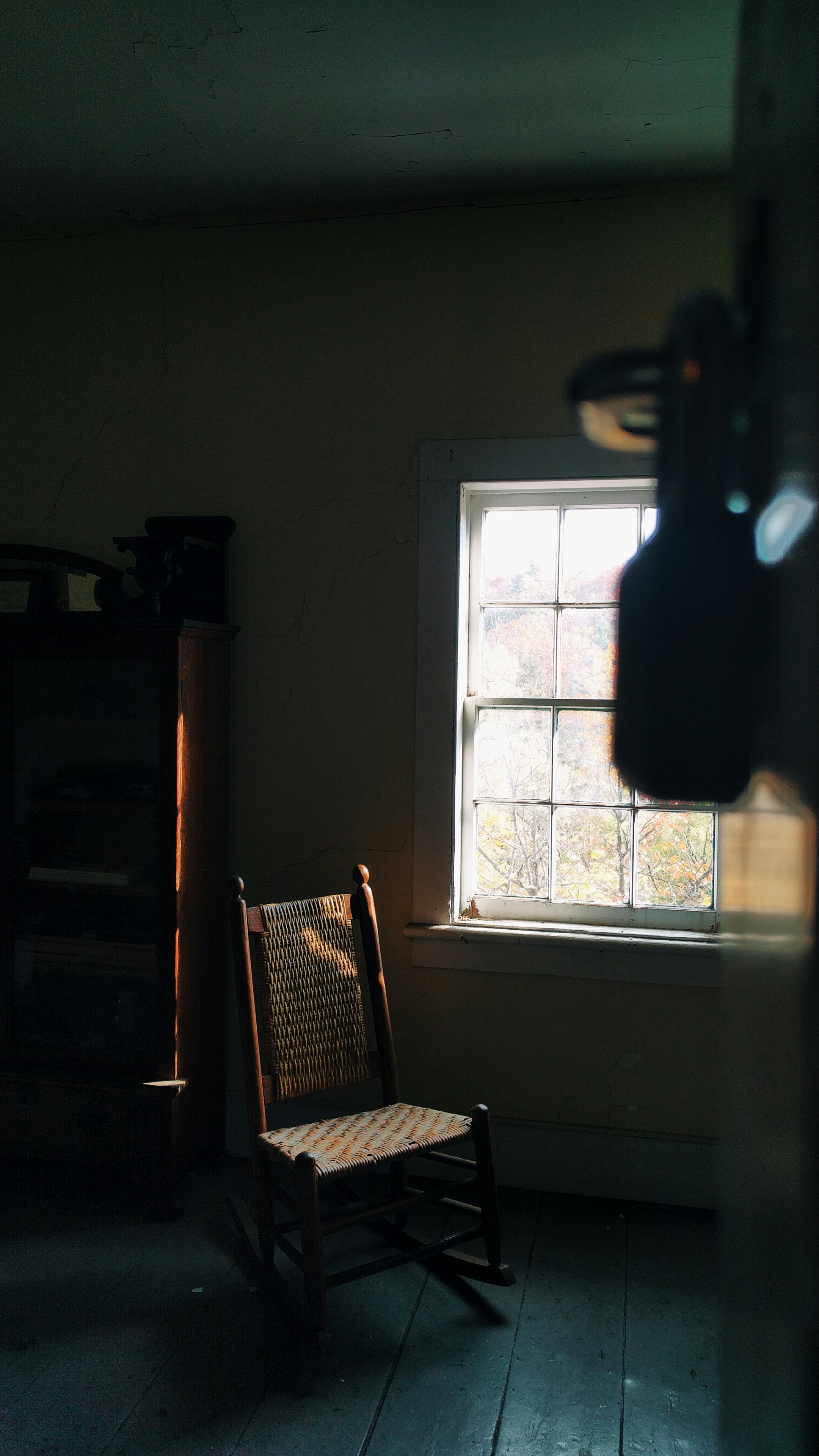A rustic rocking chair sits in a sunlit room, casting soft shadows against the walls. The warm light streaming through the window highlights the serene atmosphere.
