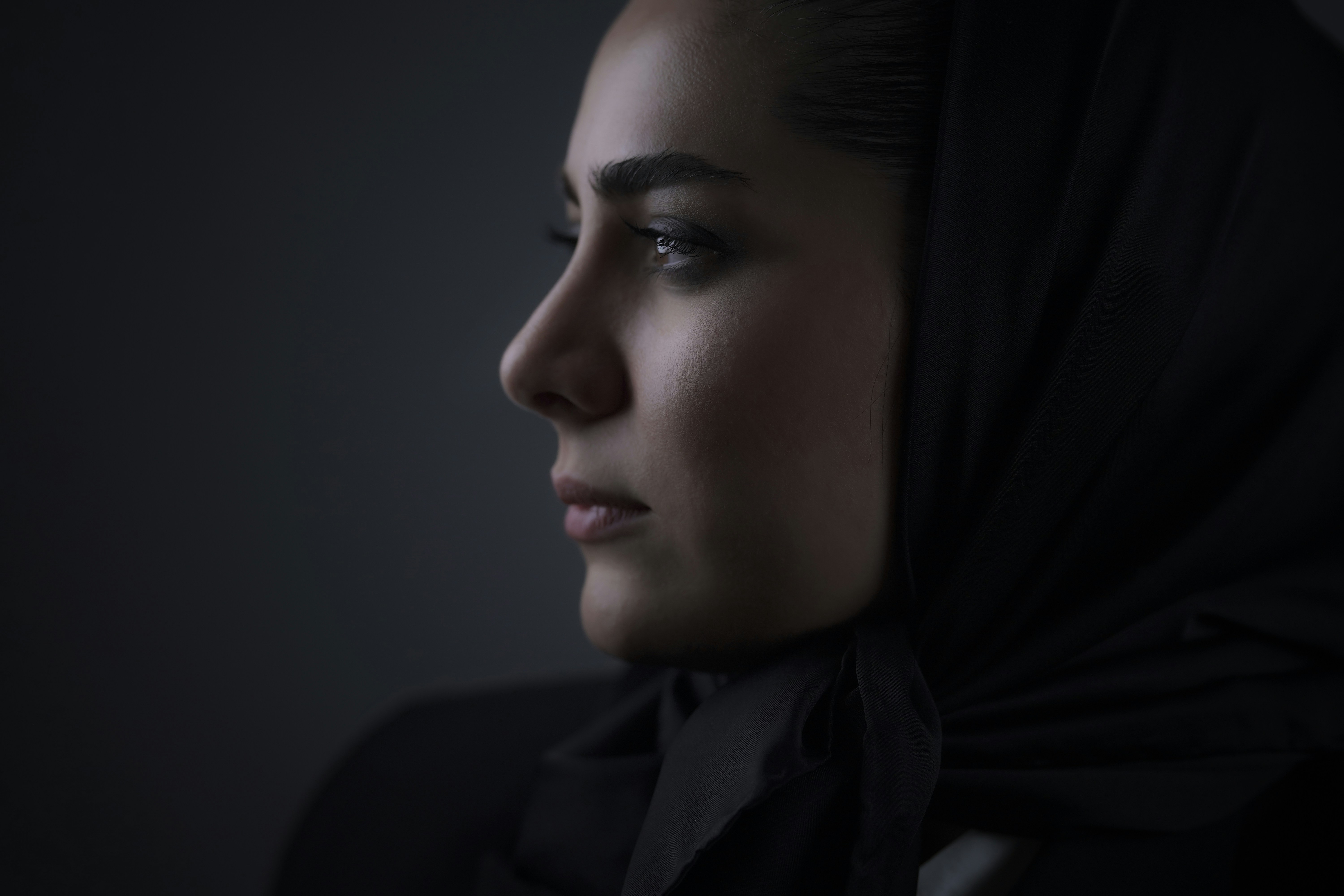Profile of a woman in a black hijab, exuding a sense of introspection against a dark backdrop.