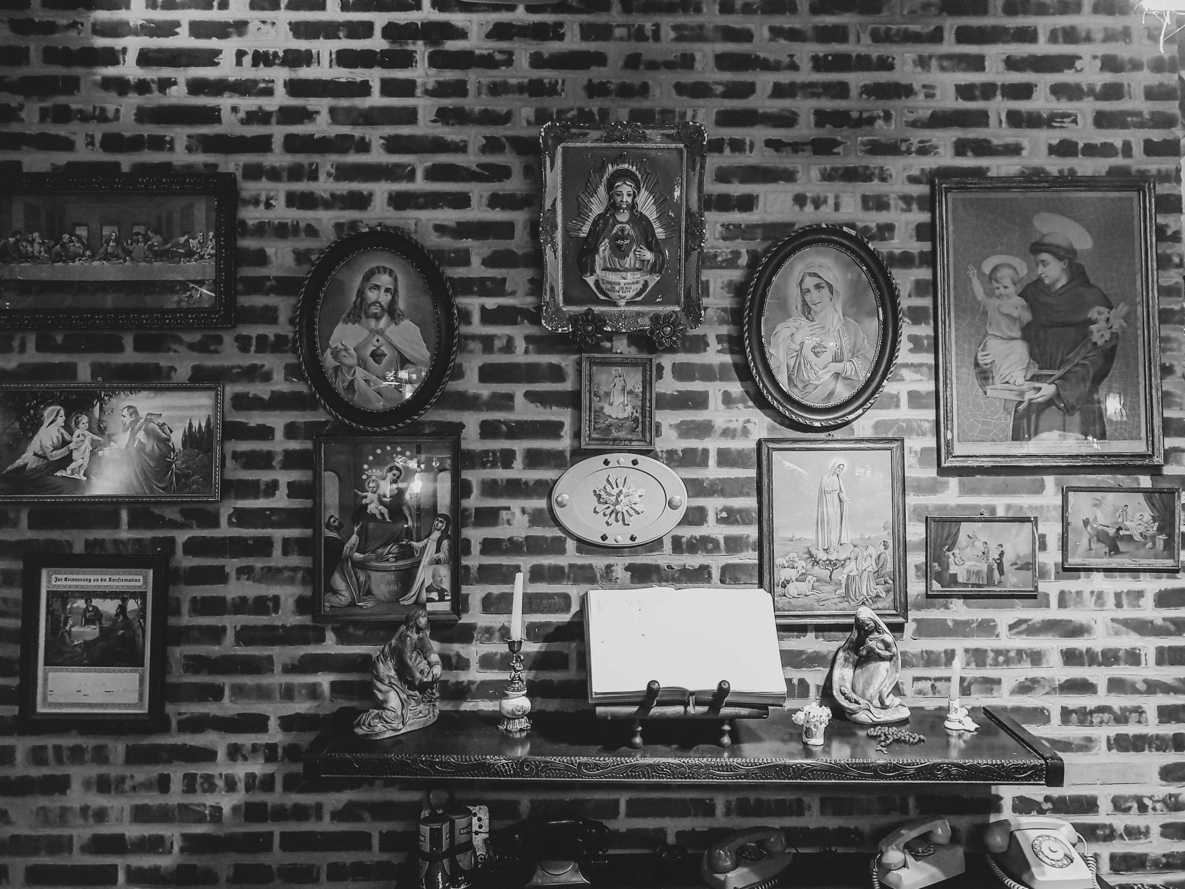 Black and white photograph of a brick wall adorned with various framed portraits and artwork.