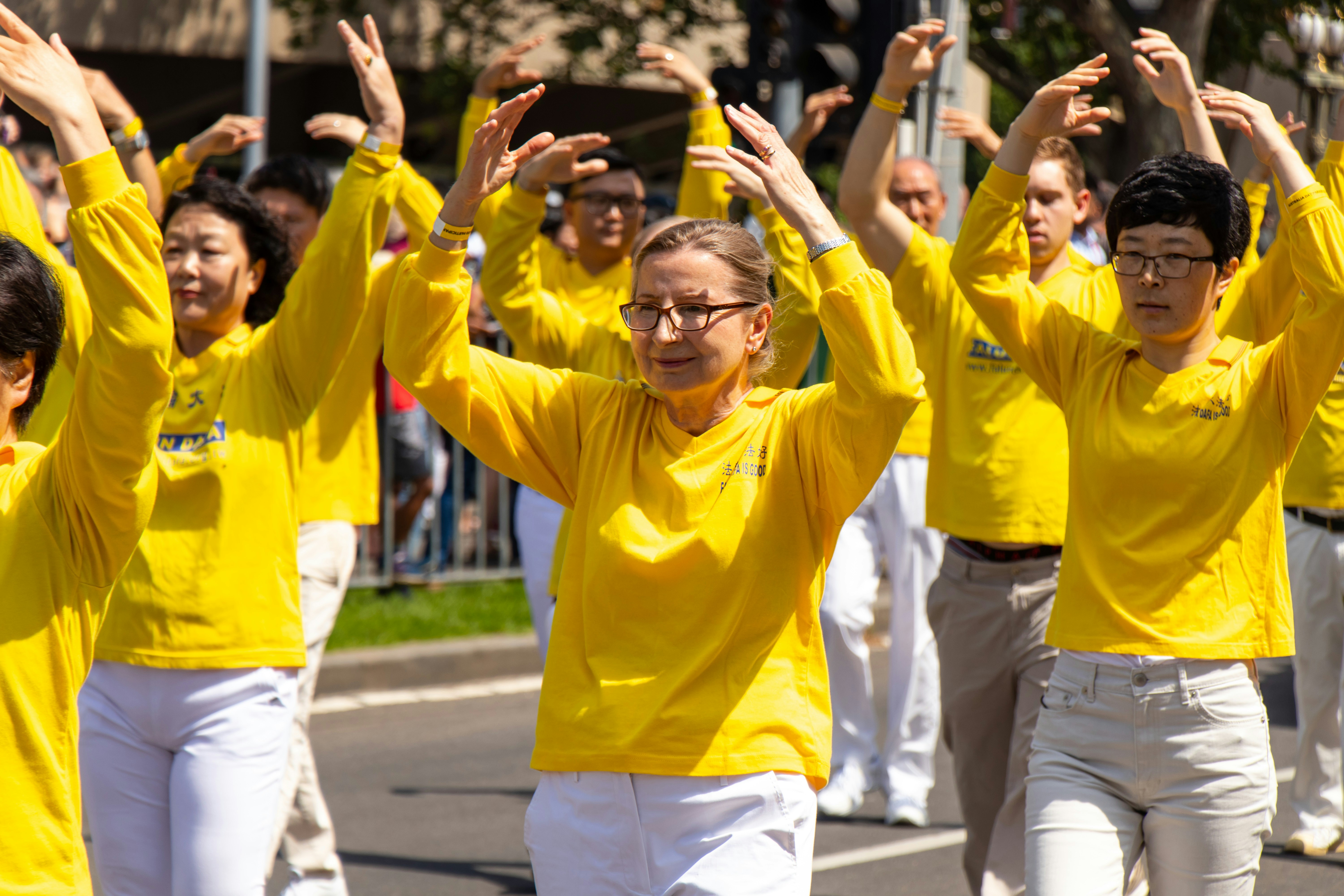 Yellow-clad dancers raise arms in a coordinated outdoor routine