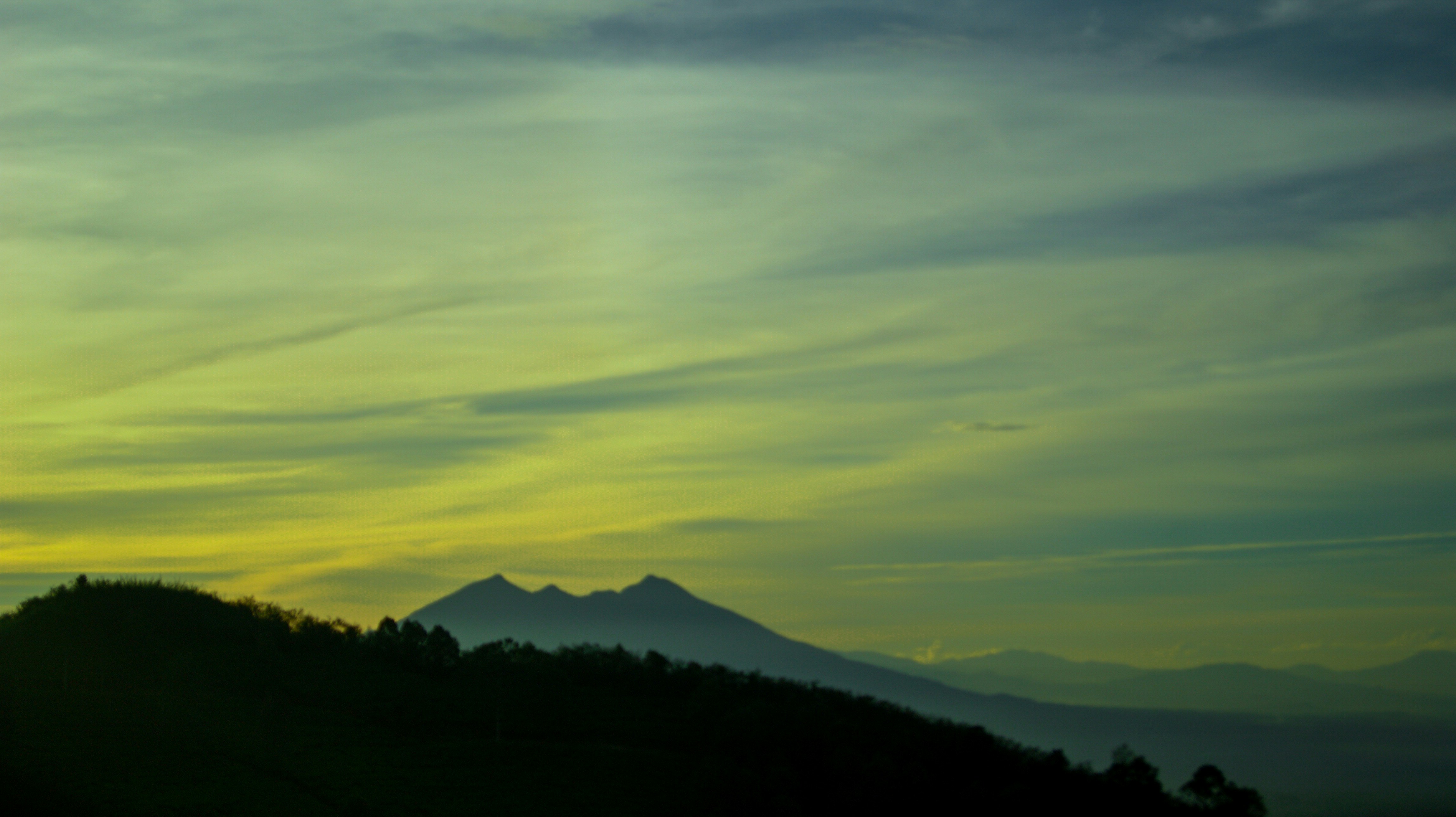 Silhouetted mountains under a gradient sky transitioning from green to blue at dawn.