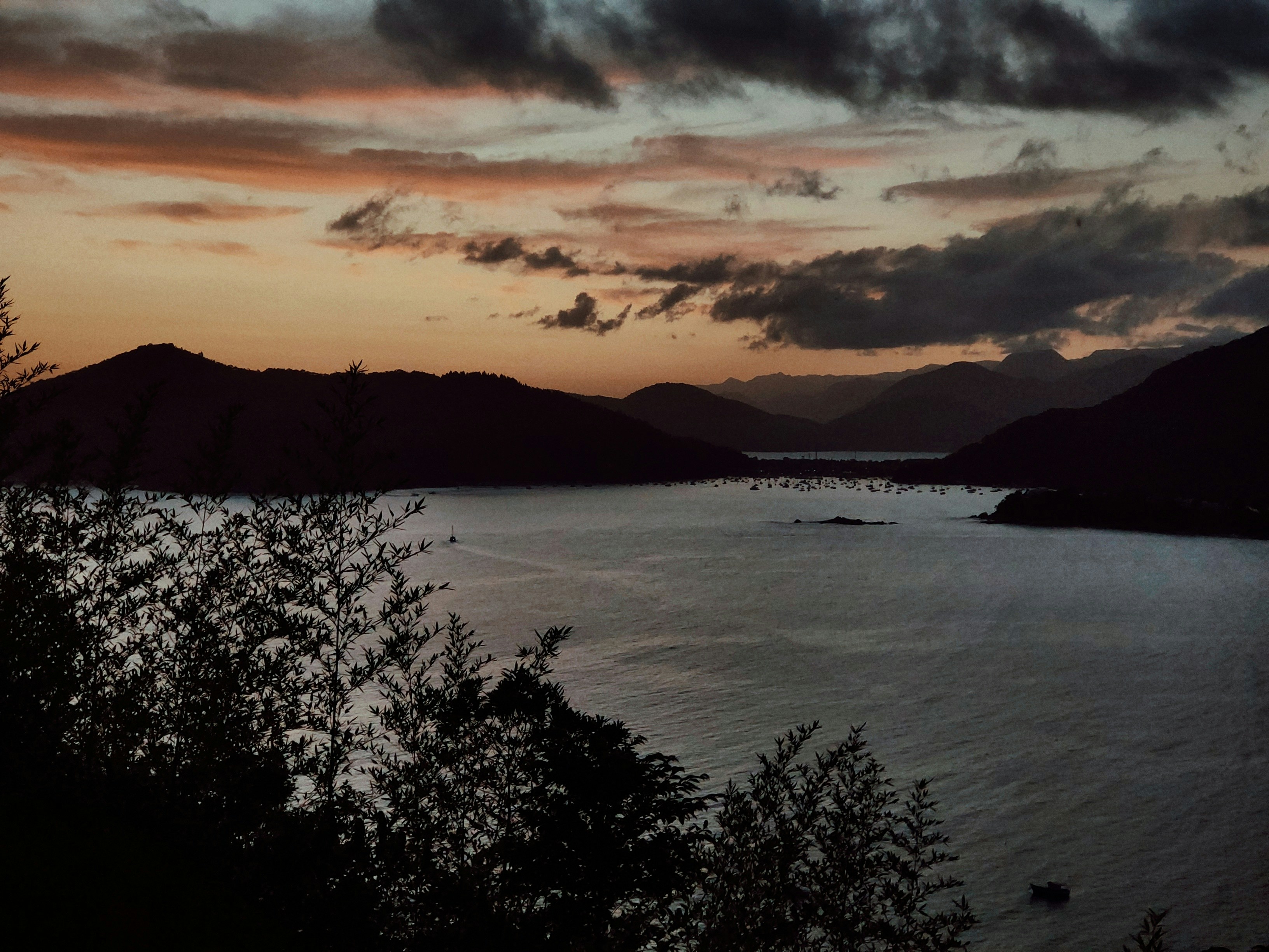 Mountain silhouettes and a tranquil body of water under a dramatic sunset sky.
