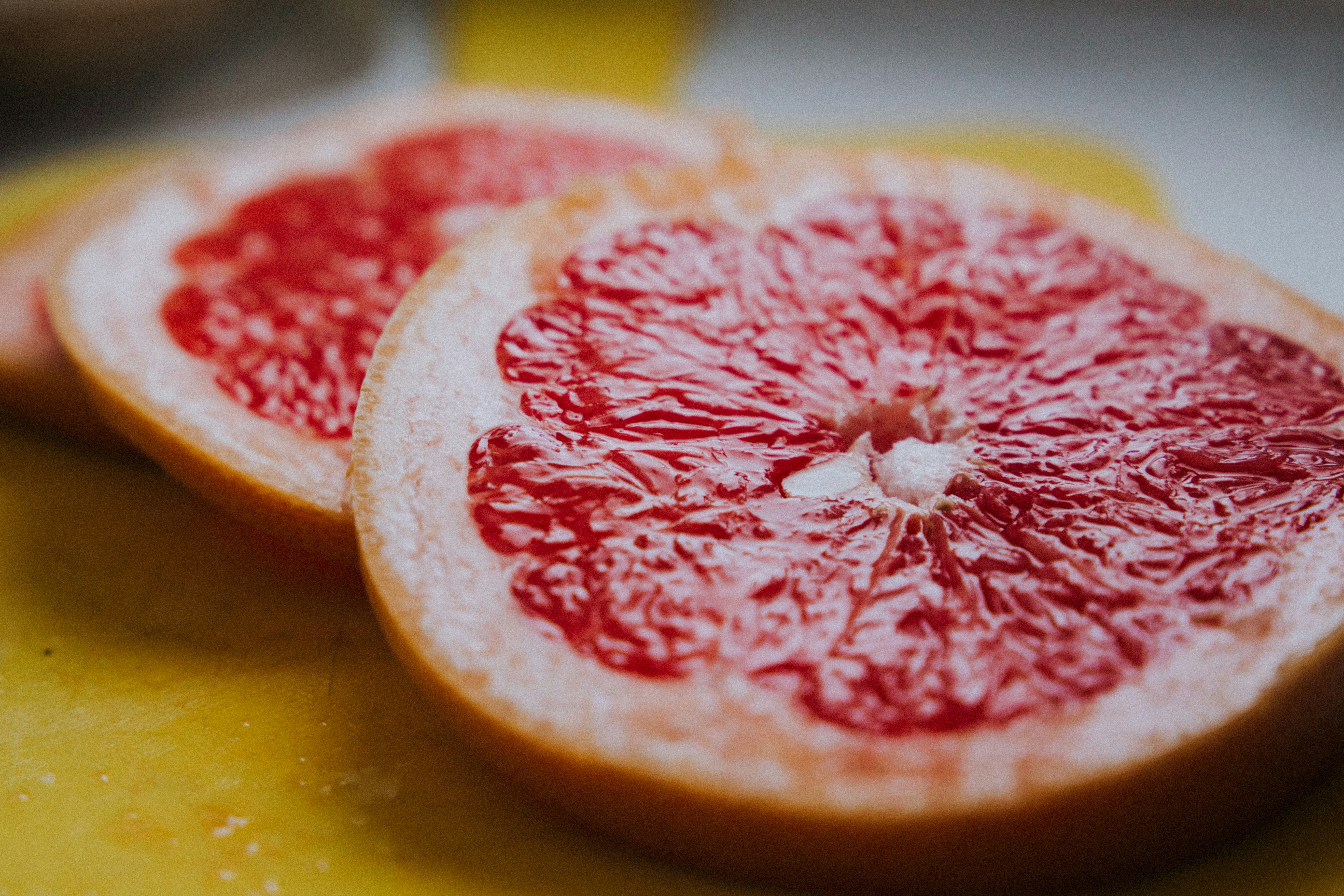 Close-up of vibrant grapefruit slices resting on a yellow cutting board, showcasing their juicy texture and rich color.