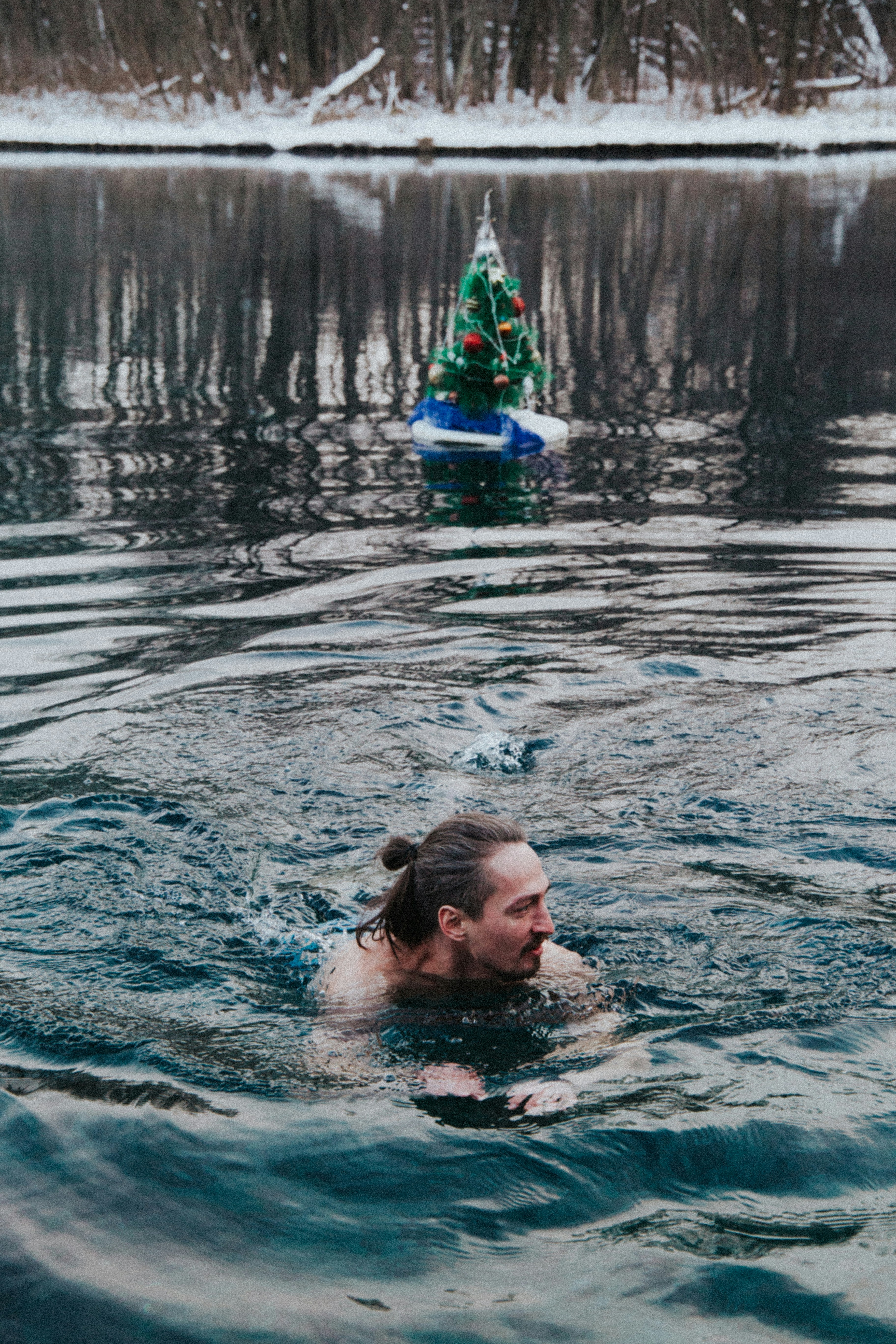 Floating Christmas: A Man Swims Toward a Decorated Boat under Winter Pines