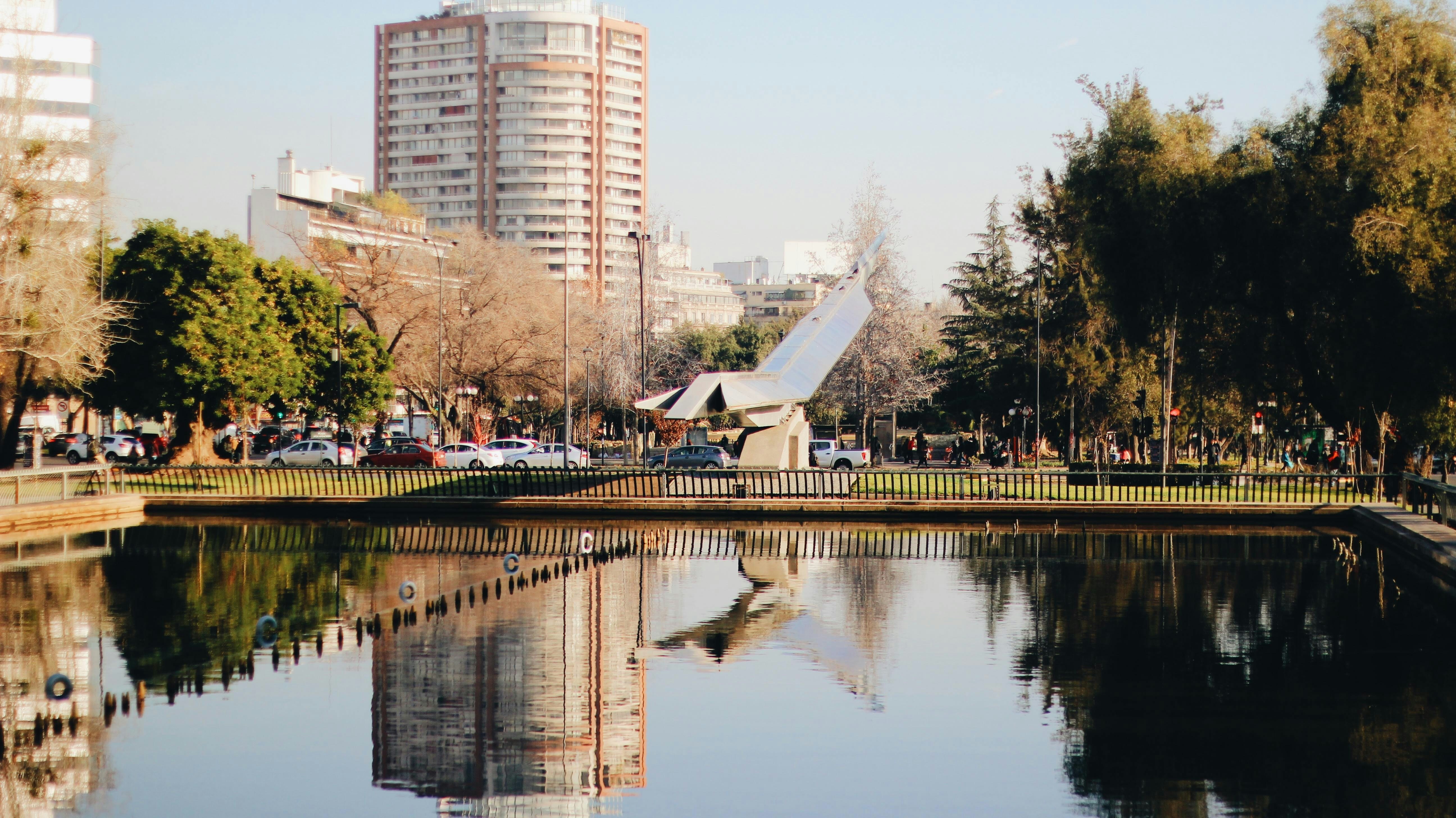 Angular White Sculpture Fracturing Reflections Across a City Park Pond