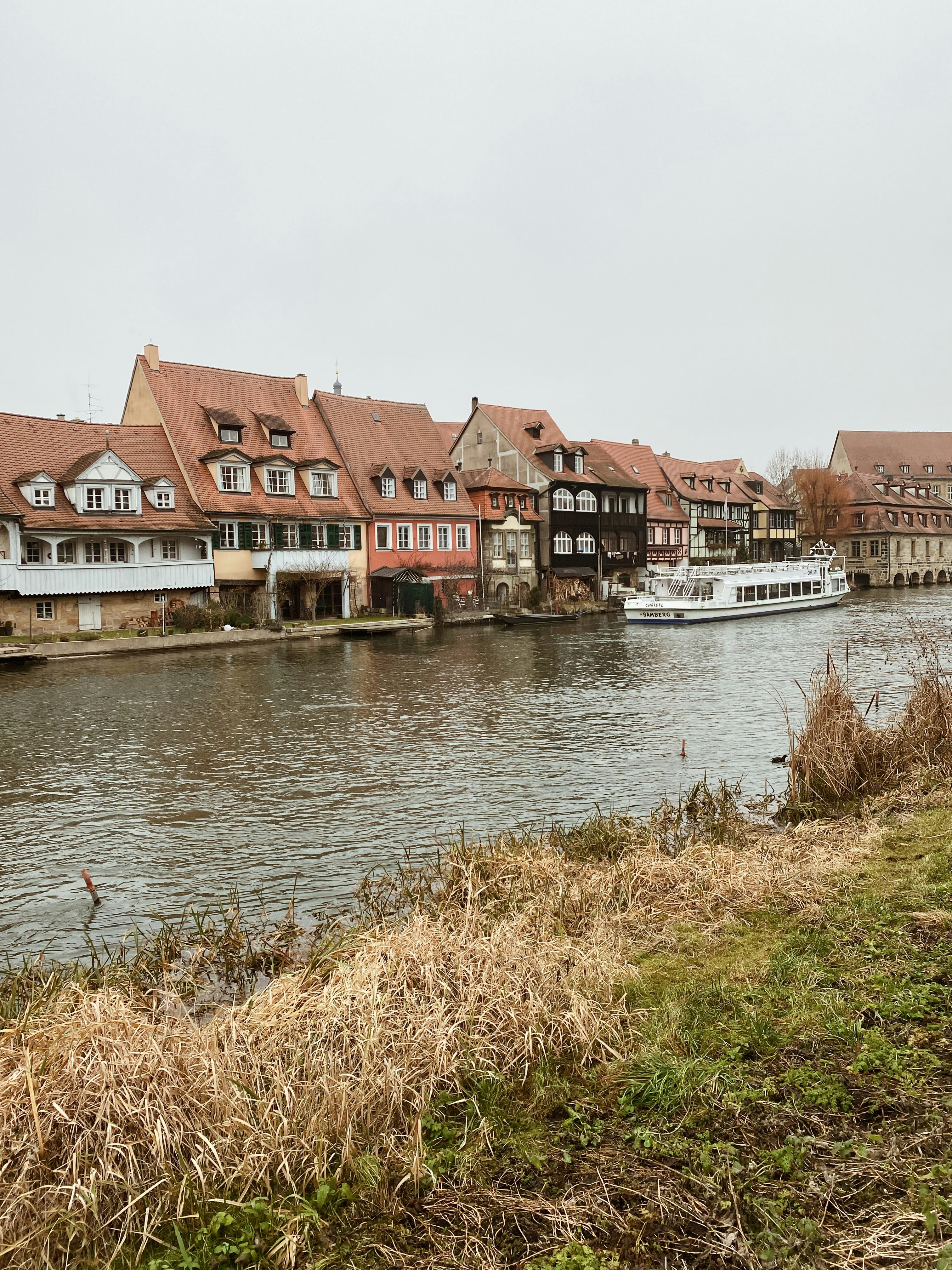Charming riverside buildings with traditional architecture lining a calm waterway, featuring a boat gently cruising by.