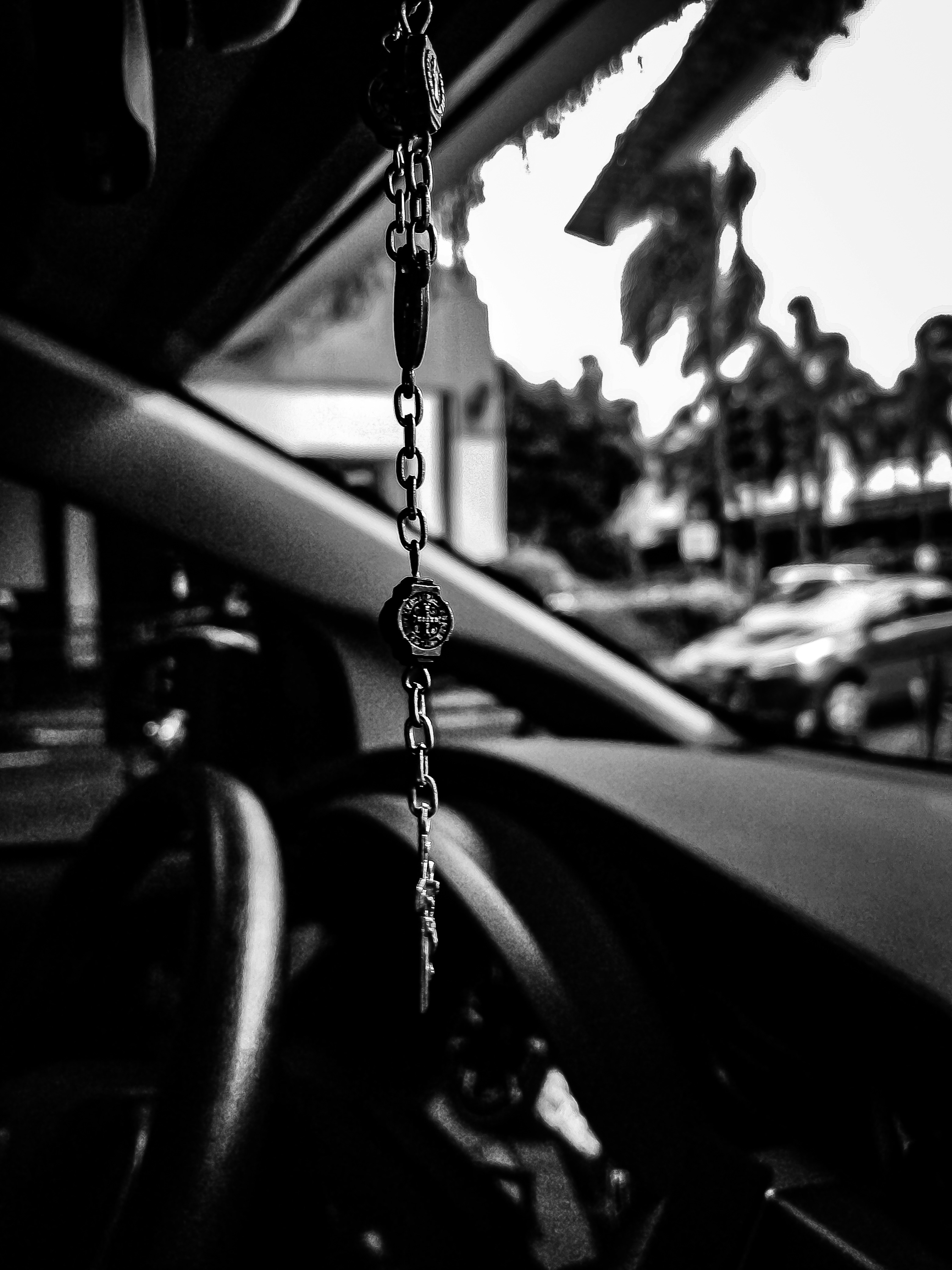 High-contrast black-and-white photograph of a hanging chain inside a car, with a blurred exterior scene in the background.