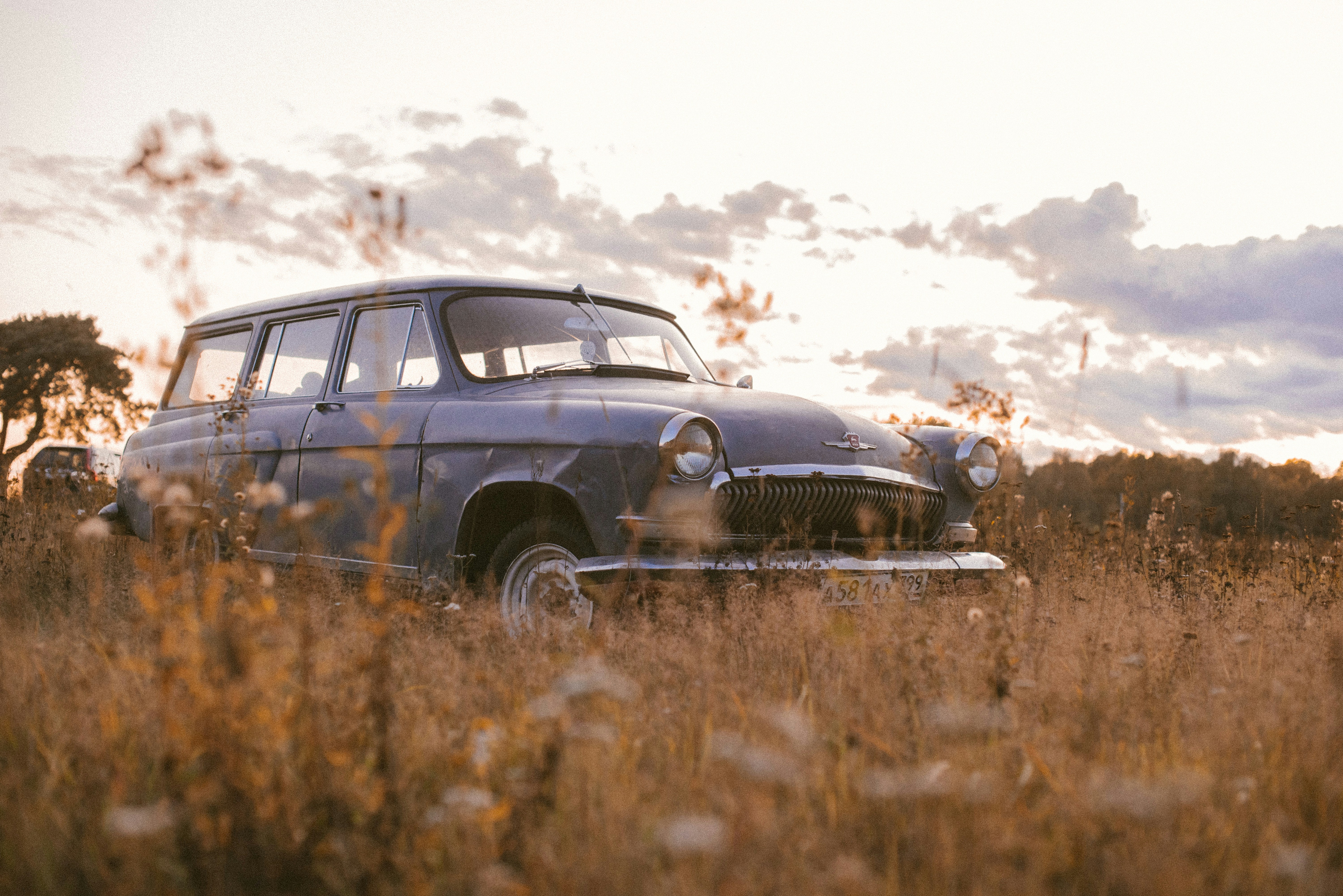 Classic Volga car parked in a field with a warm sunset sky in the background.