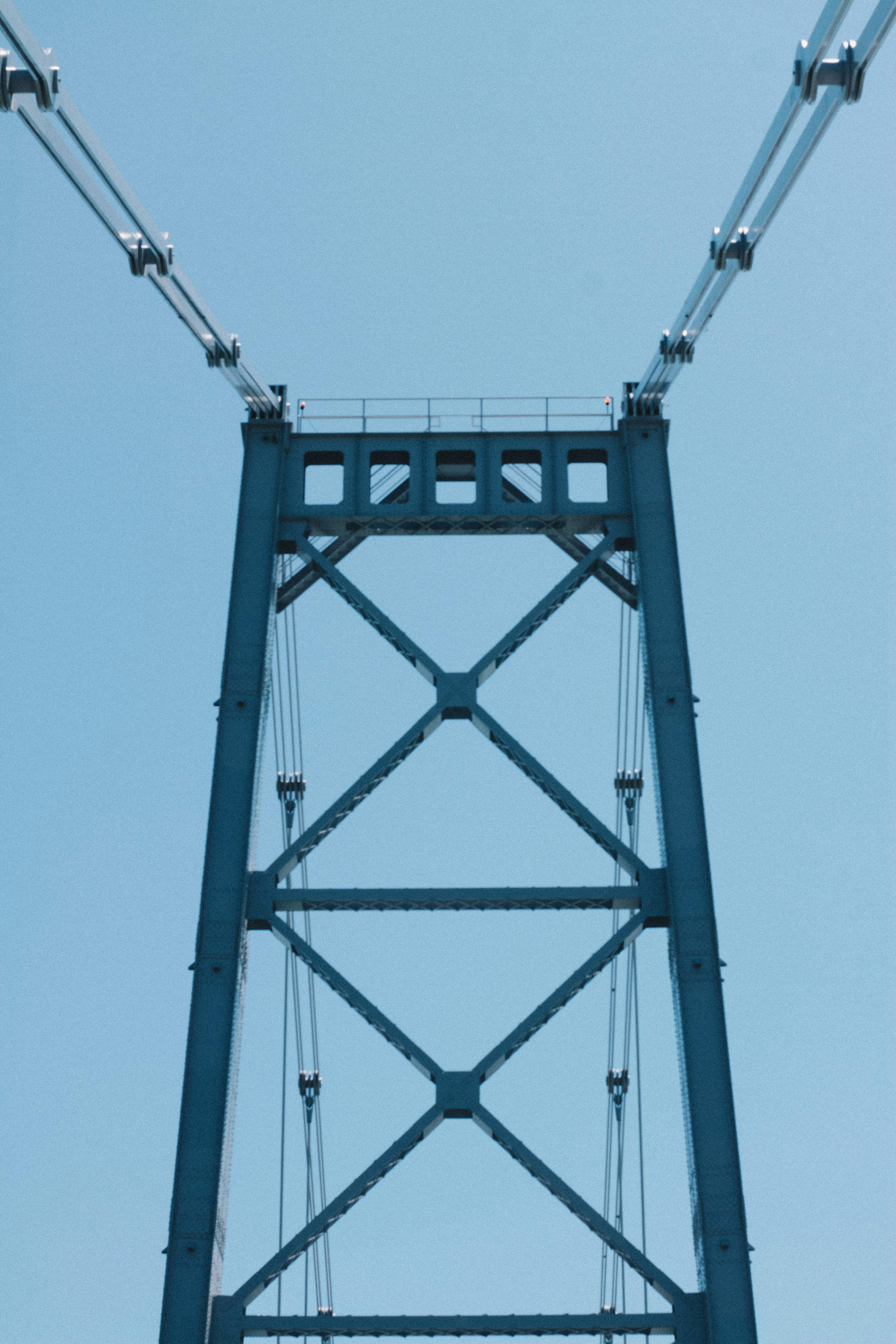 A towering bridge support structure against a clear blue sky, showcasing intricate steelwork and engineering prowess.