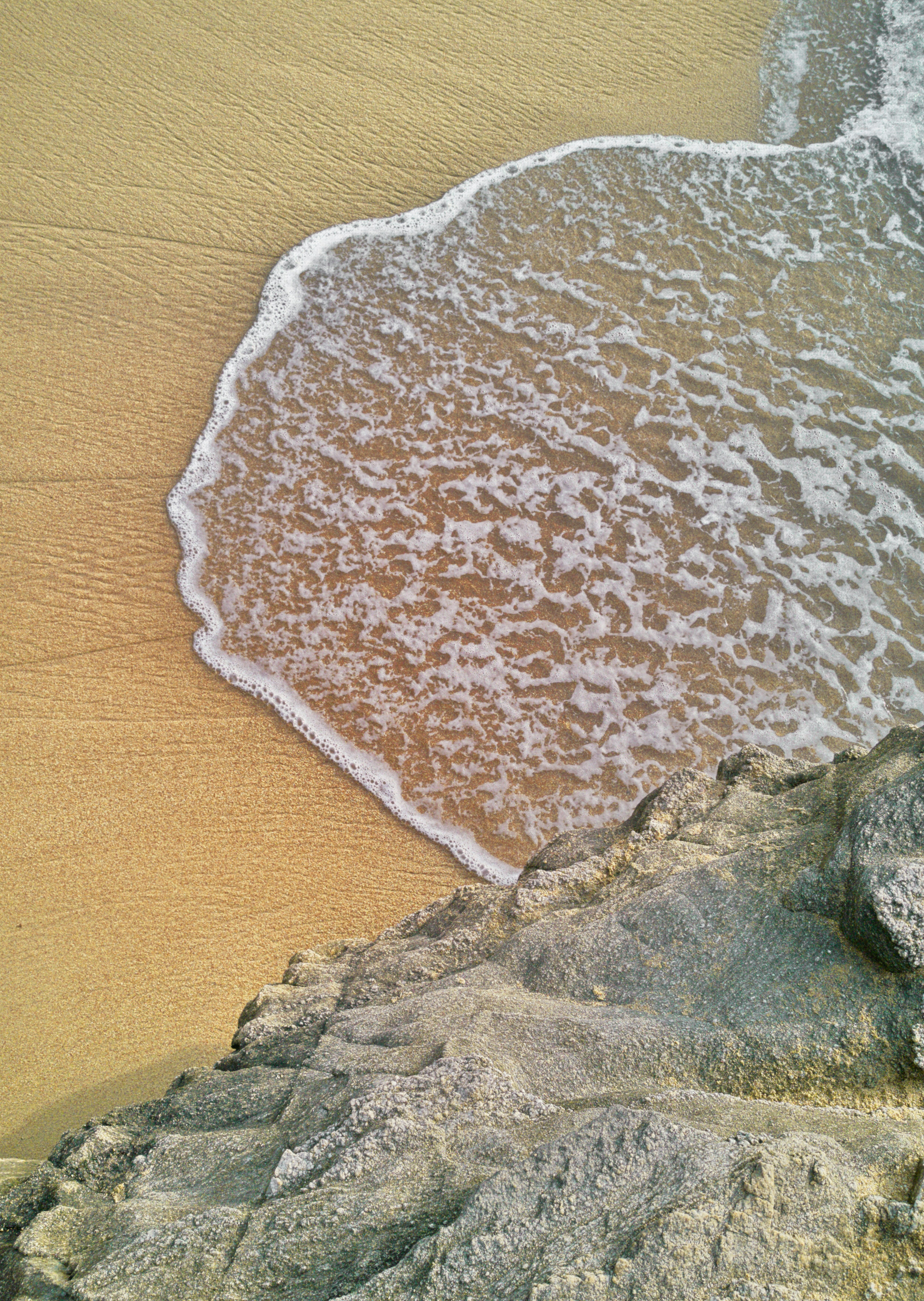 Circular foam ring on sunlit shoreline framed by rugged rocks