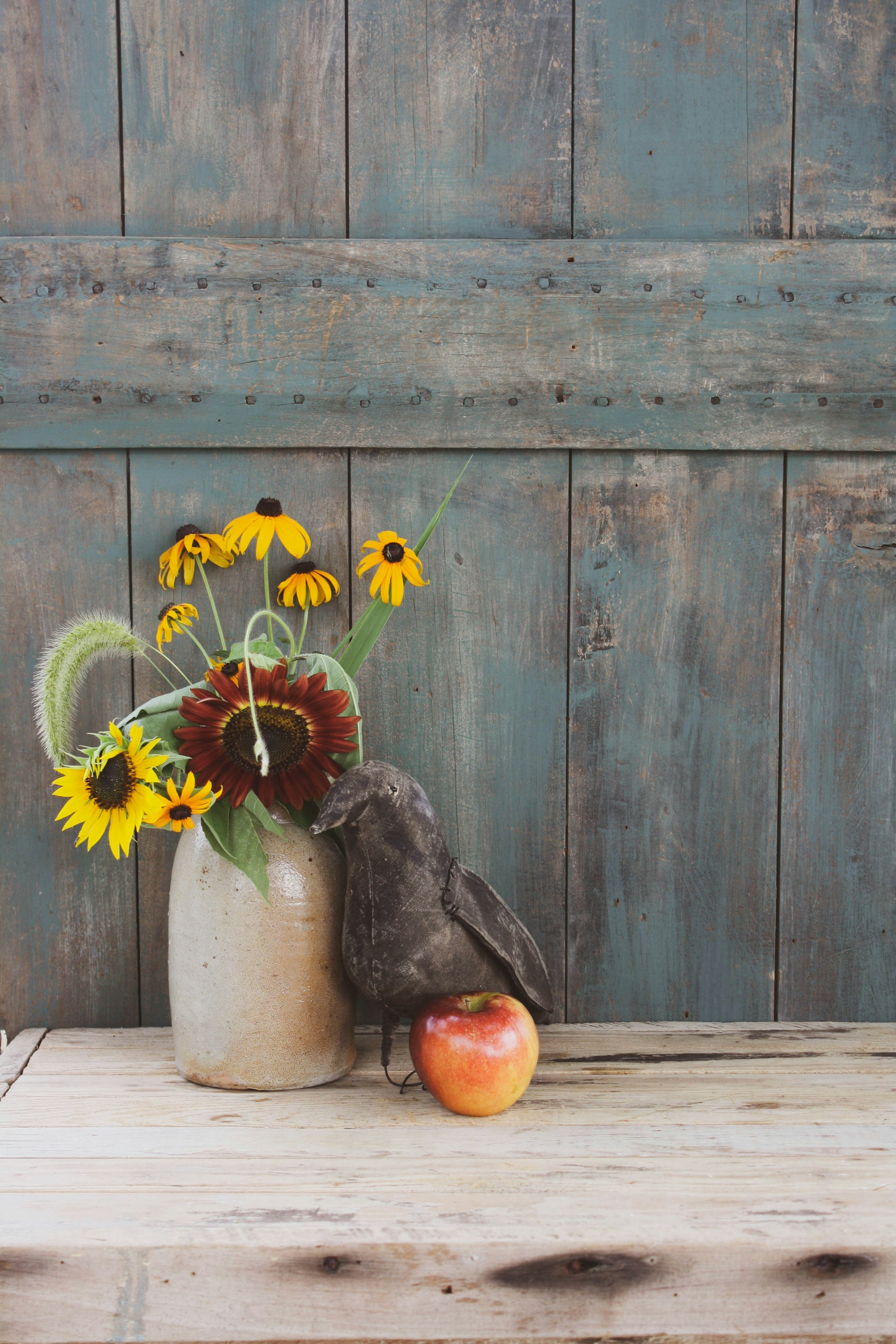 Sunflowers in a Ceramic Vase, Crow, and Apple on Weathered Blue Wood
