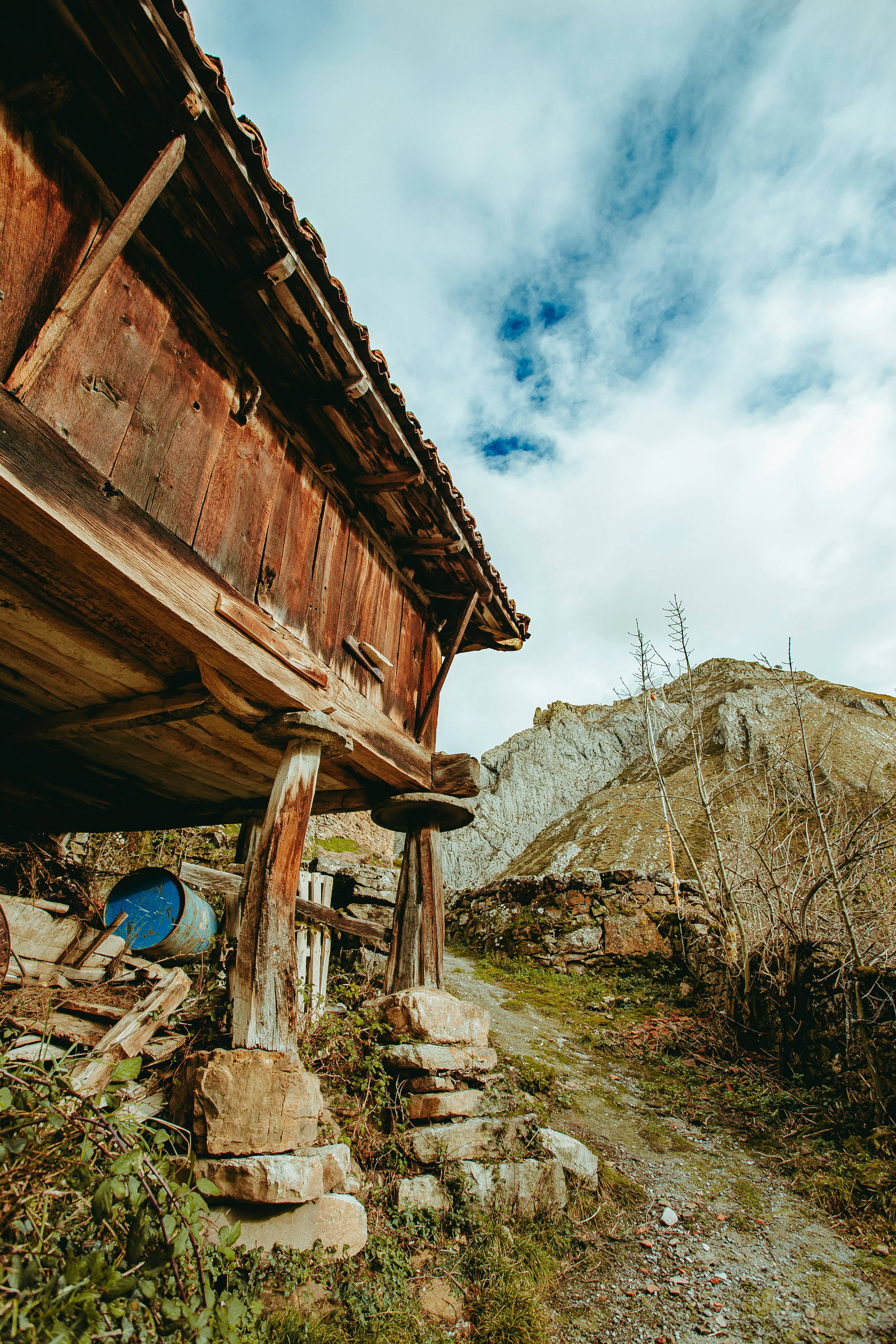 Weathered hillside cabin on stone stilts guarding a winding path toward rugged cliffs