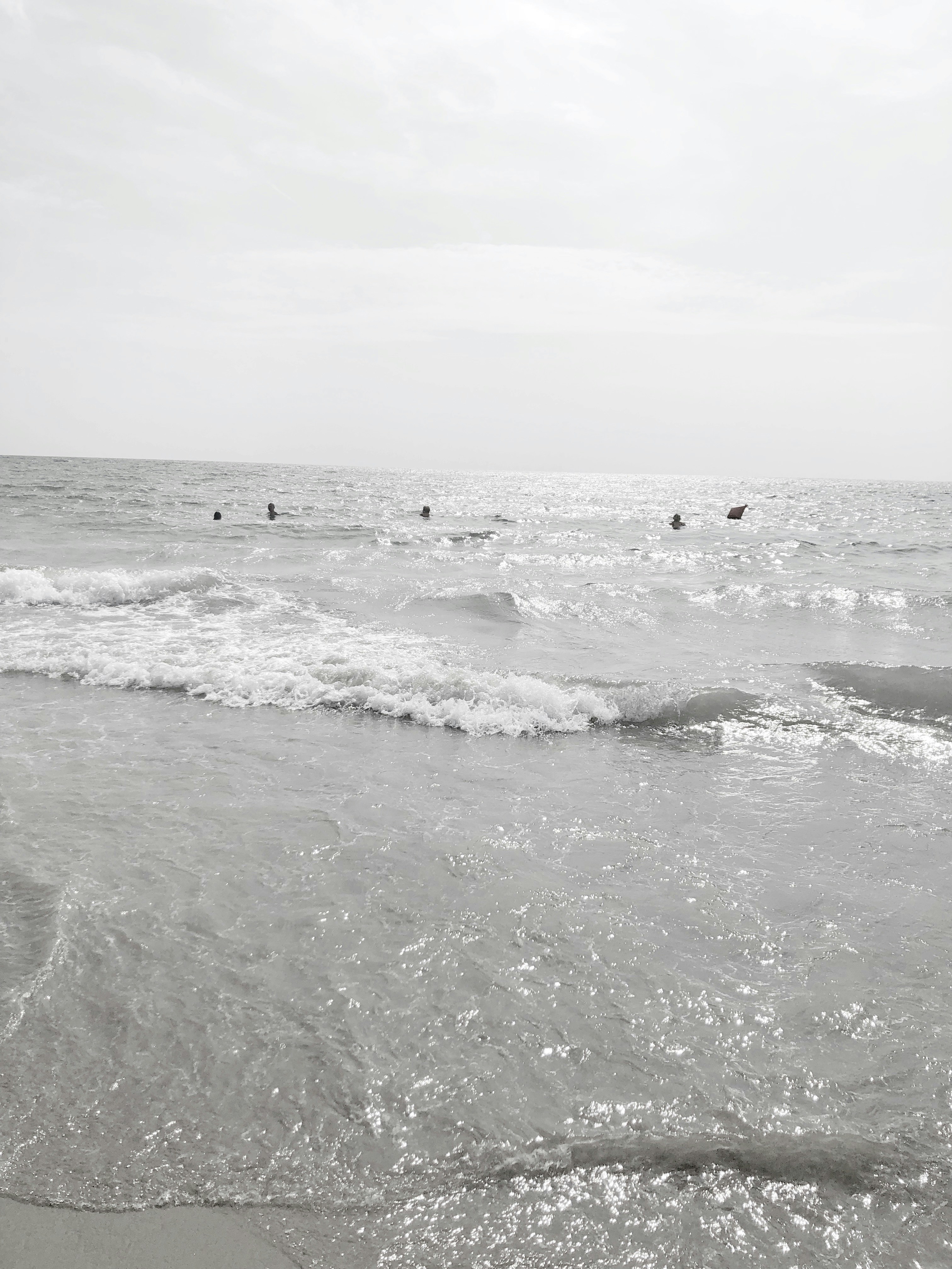 Gentle waves lapping at a sandy beach with distant figures enjoying the water. The scene evokes a tranquil summer day.