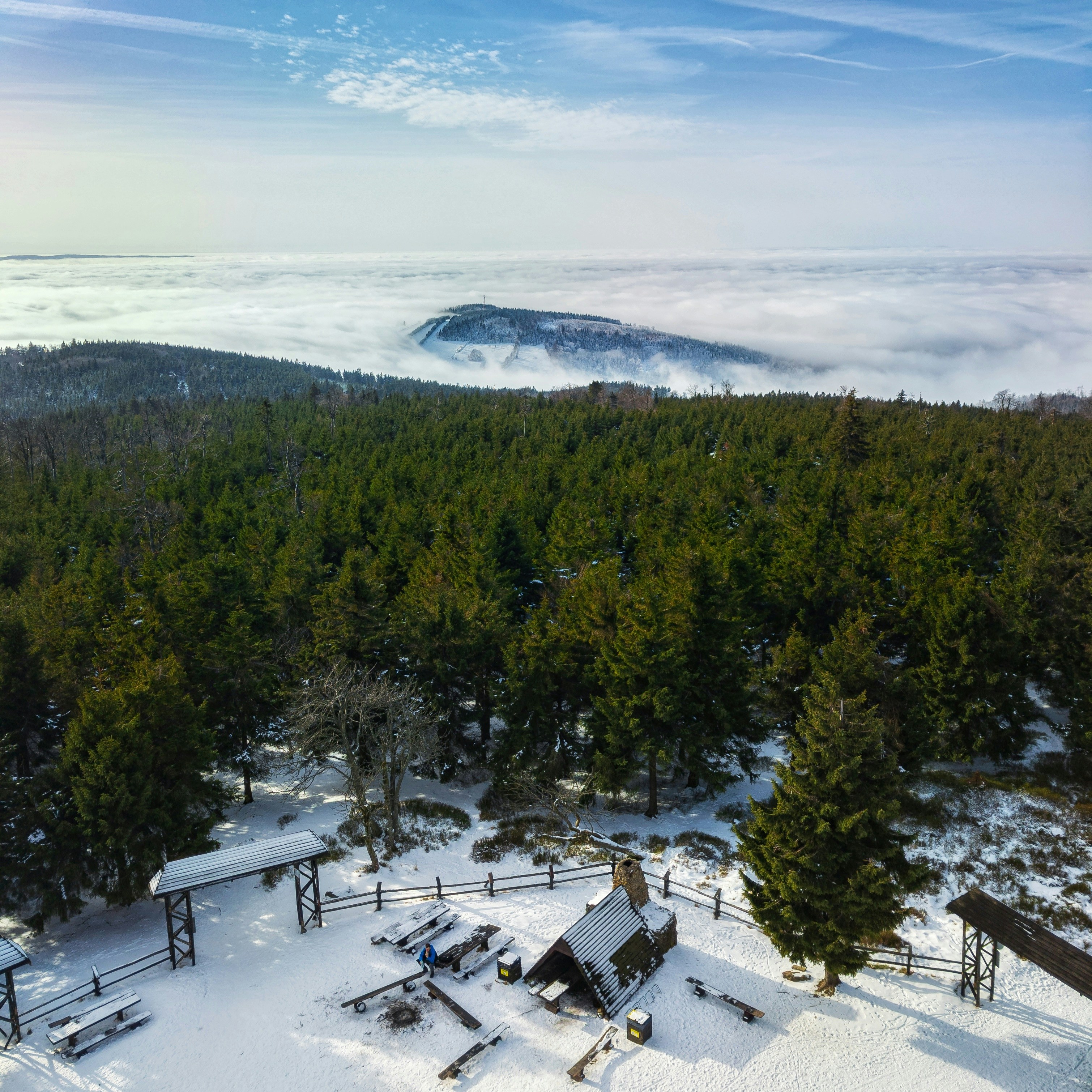 Snow-covered forest landscape with distant mountains peeking through a blanket of clouds.