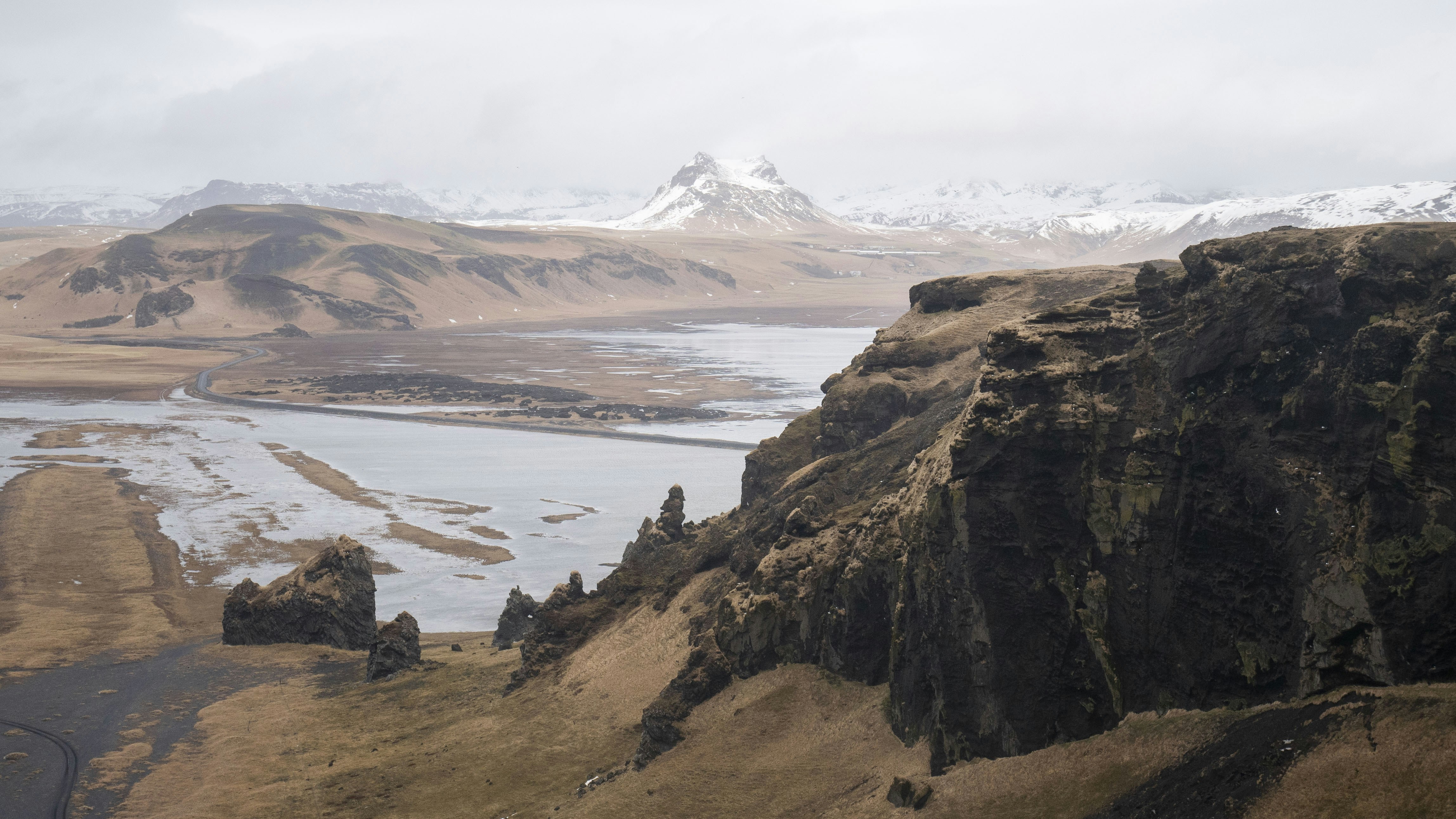 Cliffside Ridge Over a Winding Delta under Misty Peaks