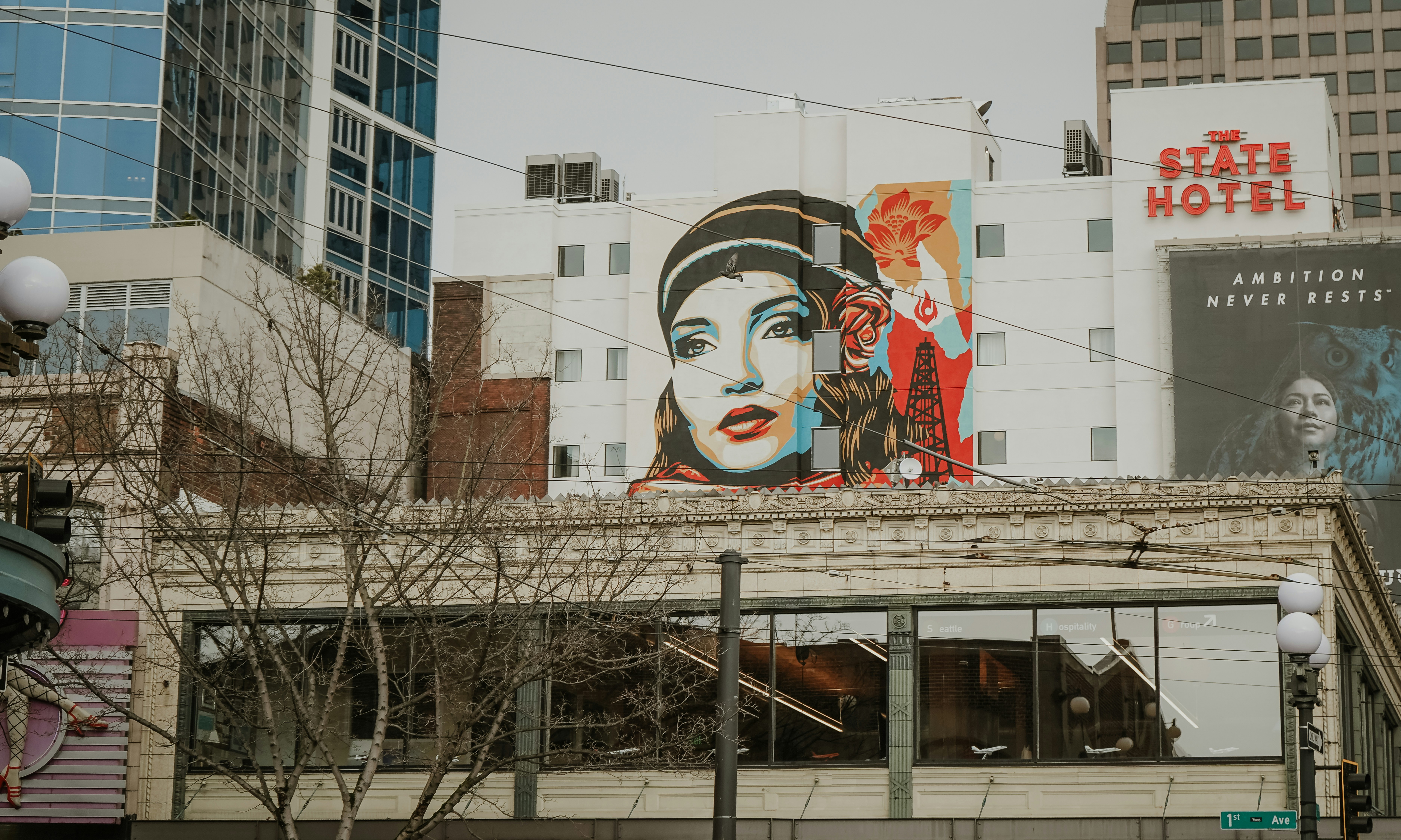 Vibrant mural of a woman's face on a city building facade in Seattle, with surrounding architecture under a gray sky.