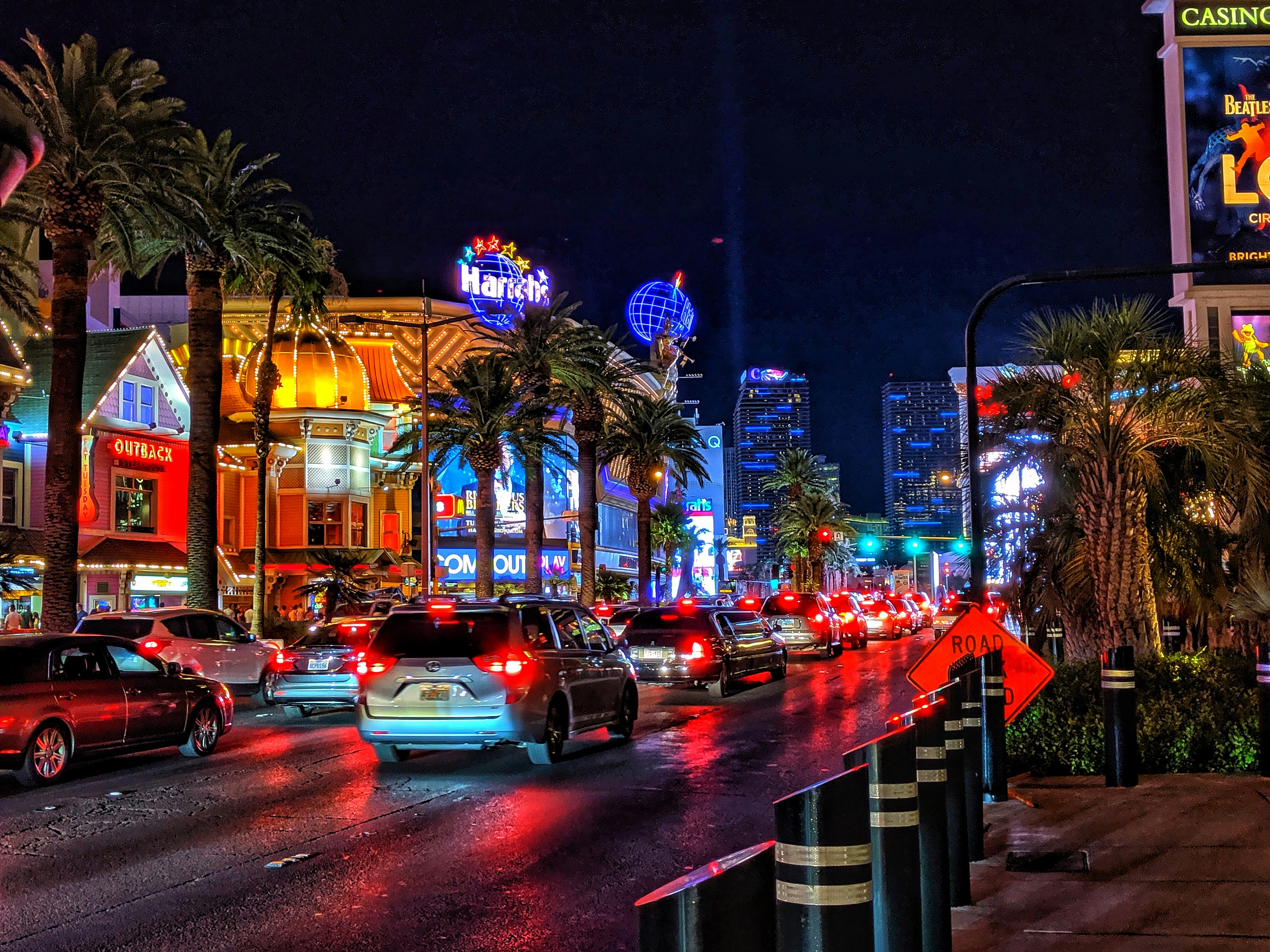 Neon-lit street bustling with cars under a night sky, surrounded by illuminated buildings and palm trees.