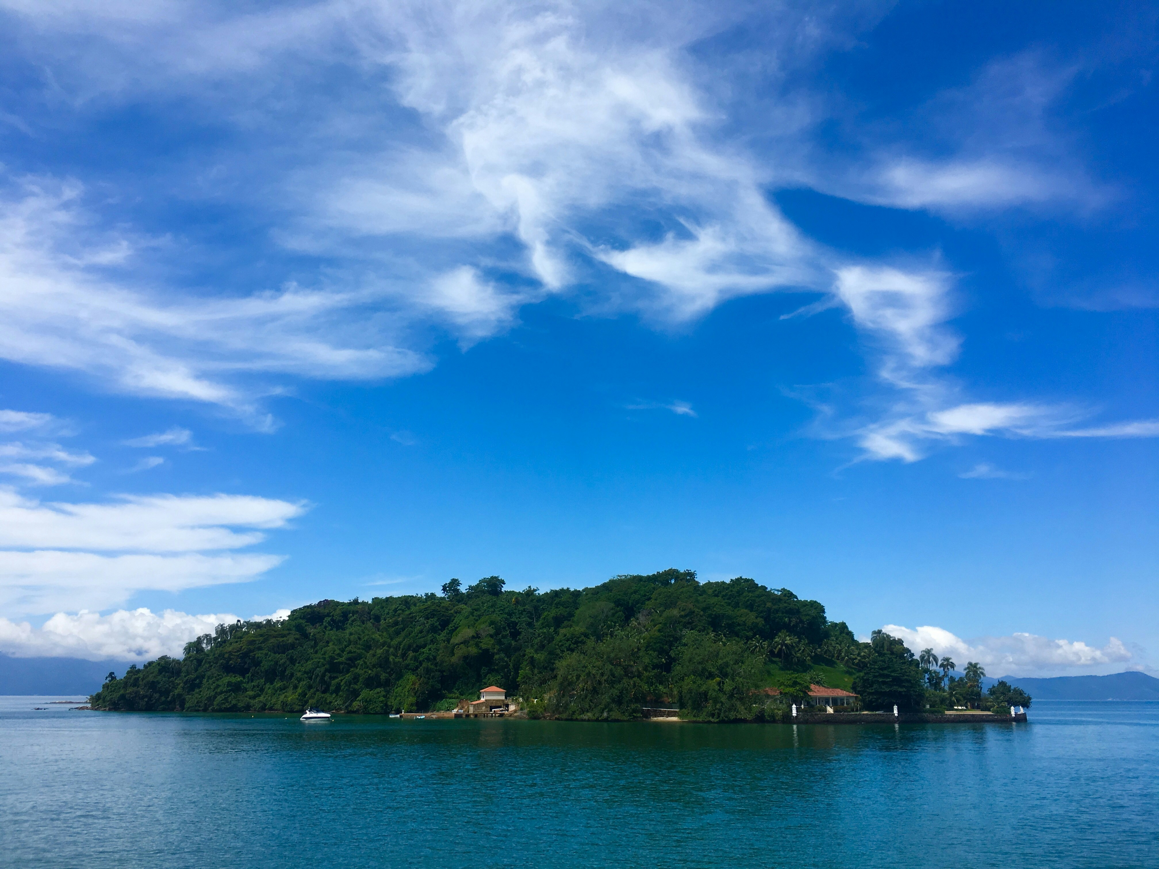 Lush green island surrounded by vibrant blue waters beneath a sky painted with wispy clouds.