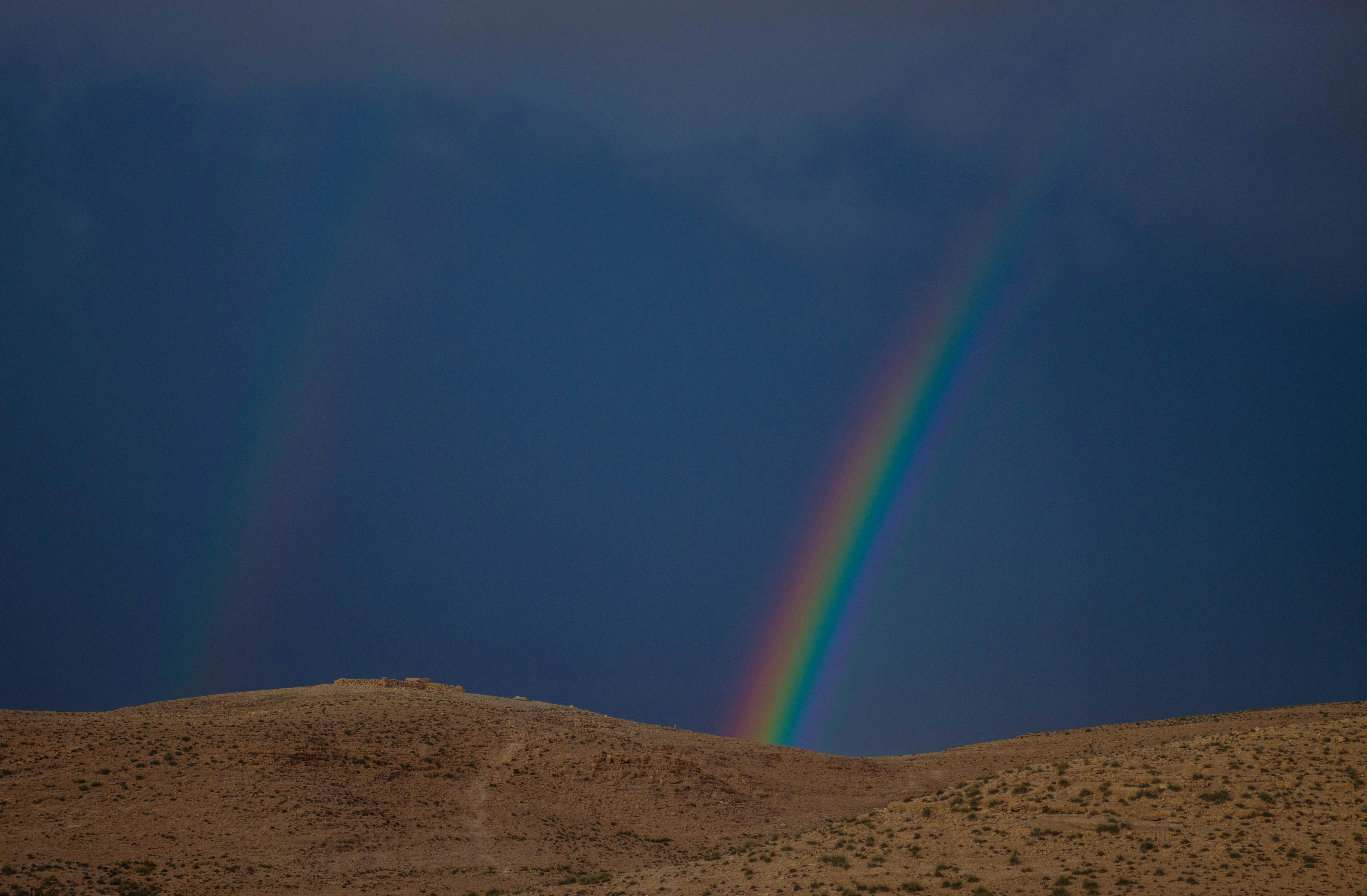 Vibrant rainbow arcs over a barren landscape, contrasting against dark storm clouds. The scene evokes a sense of hope and tranquility.