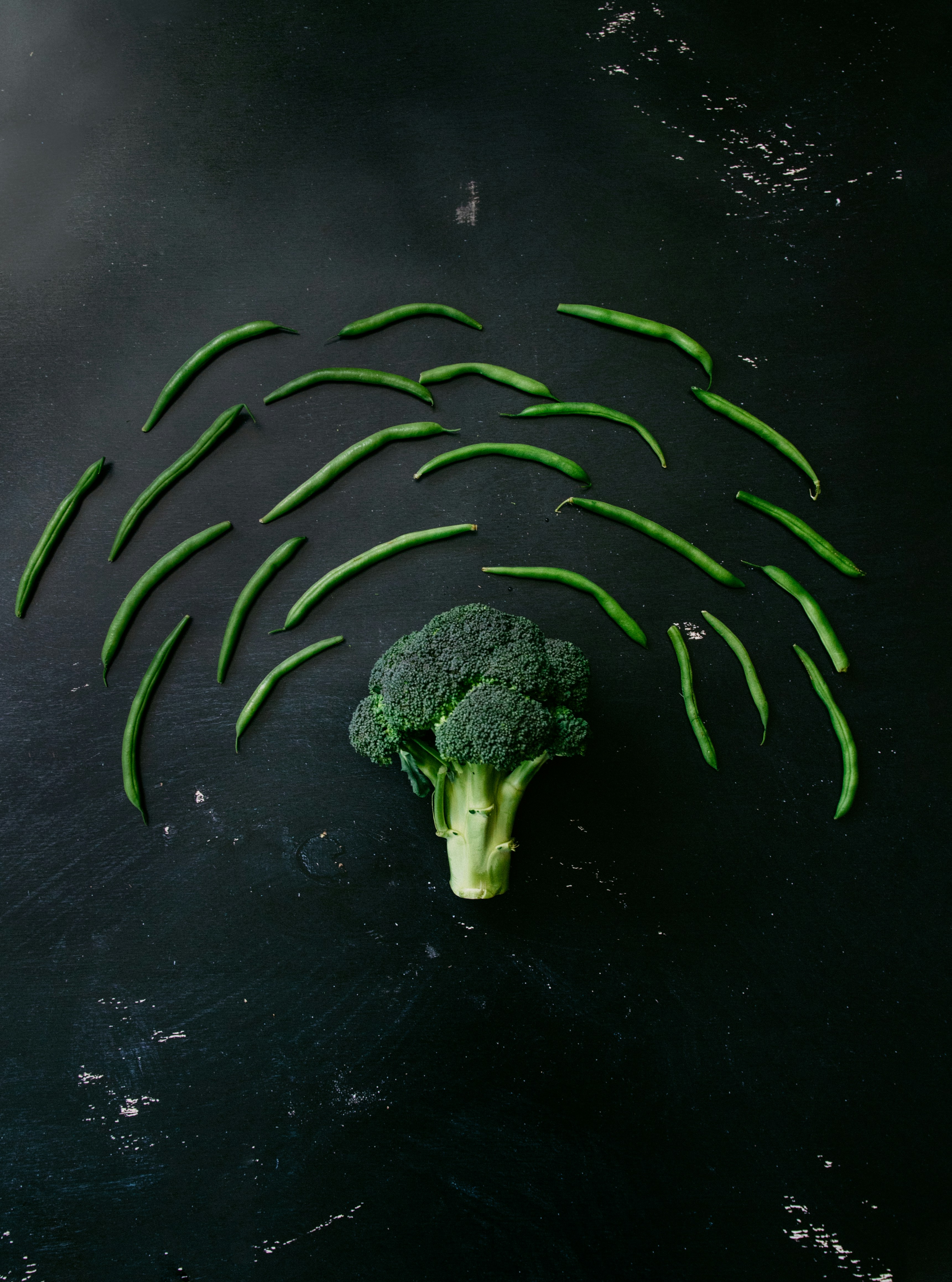 Broccoli stands at the center, surrounded by artistically arranged green beans, creating a visual melody of fresh produce.