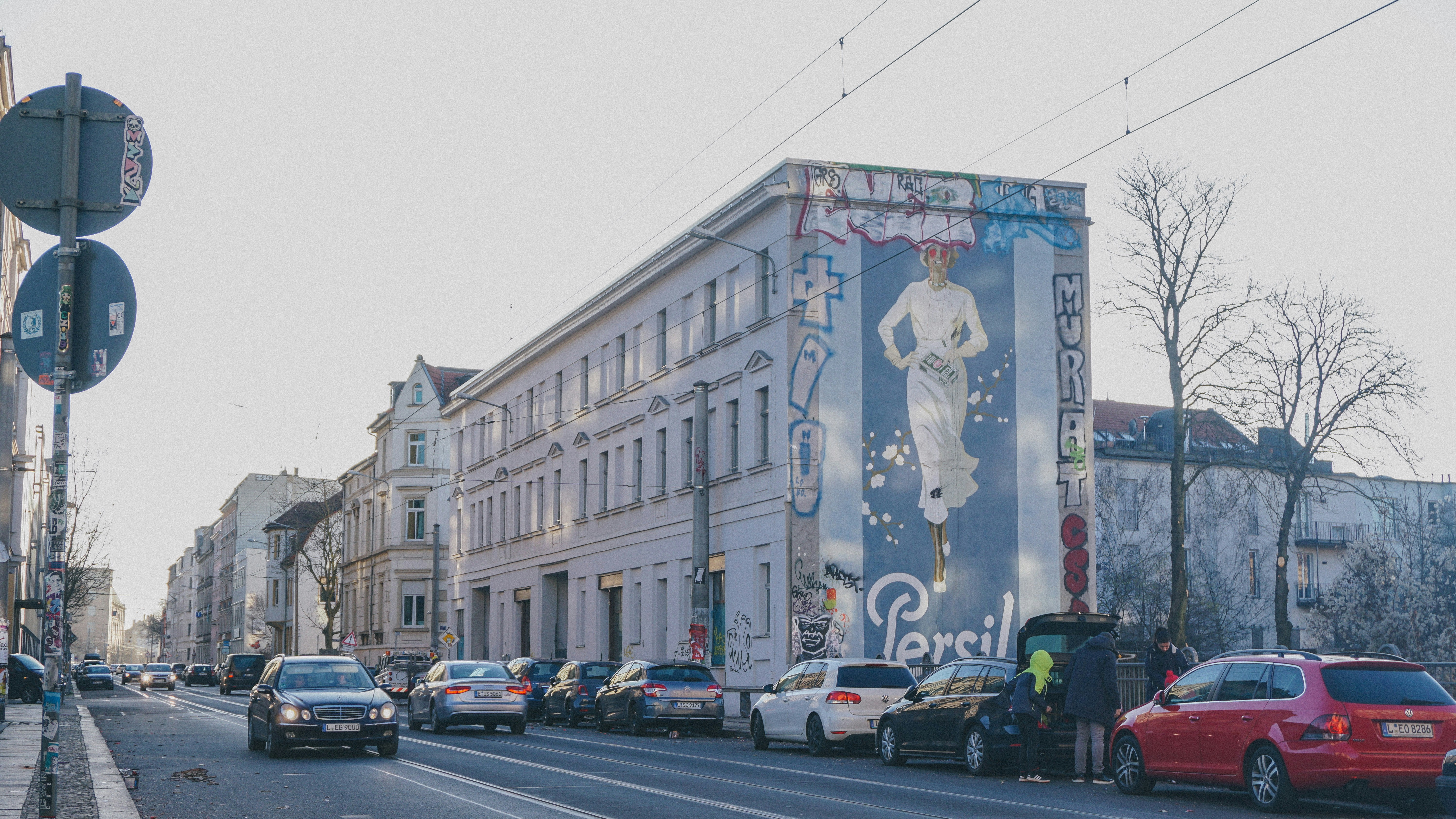 Vibrant mural depicting a woman in white against an urban backdrop, showcasing the brand Persil. The scene captures the essence of street art in a bustling city environment.