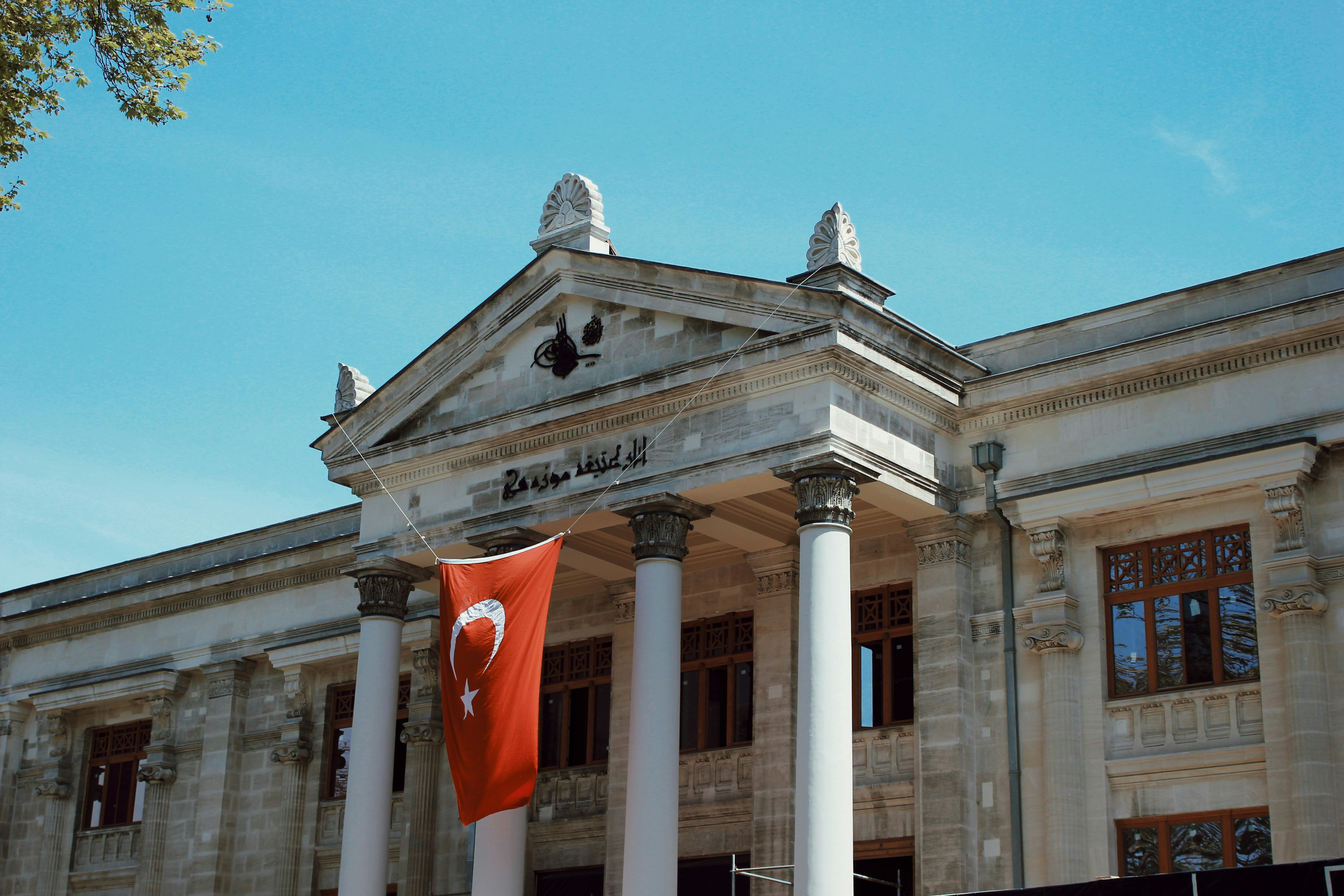 Historic building facade featuring classical architecture with a prominent Turkish flag hanging in front.
