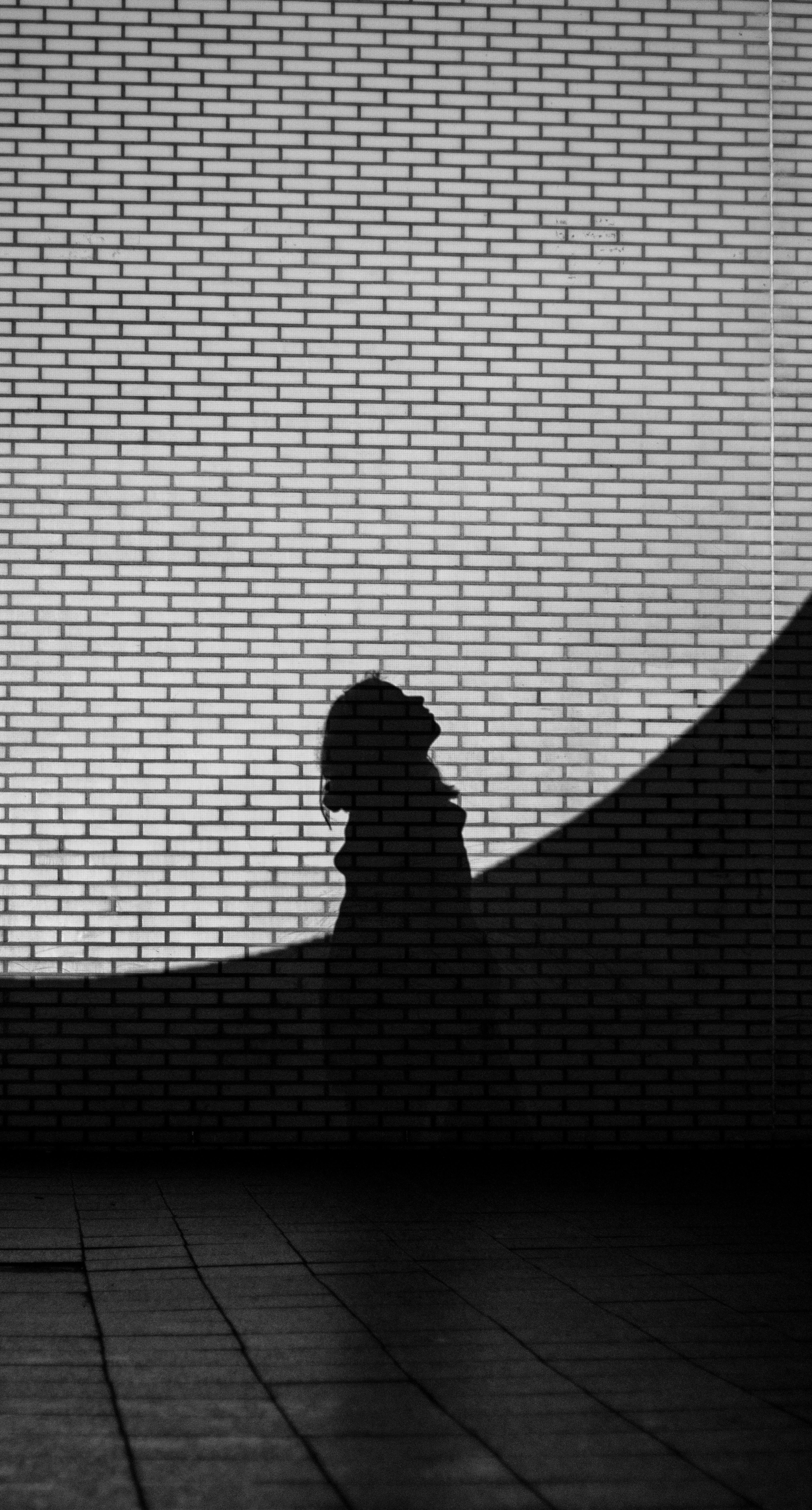 Silhouette of a figure against a textured wall, illuminated by a soft circular light, creating an intriguing interplay of shadow and form.