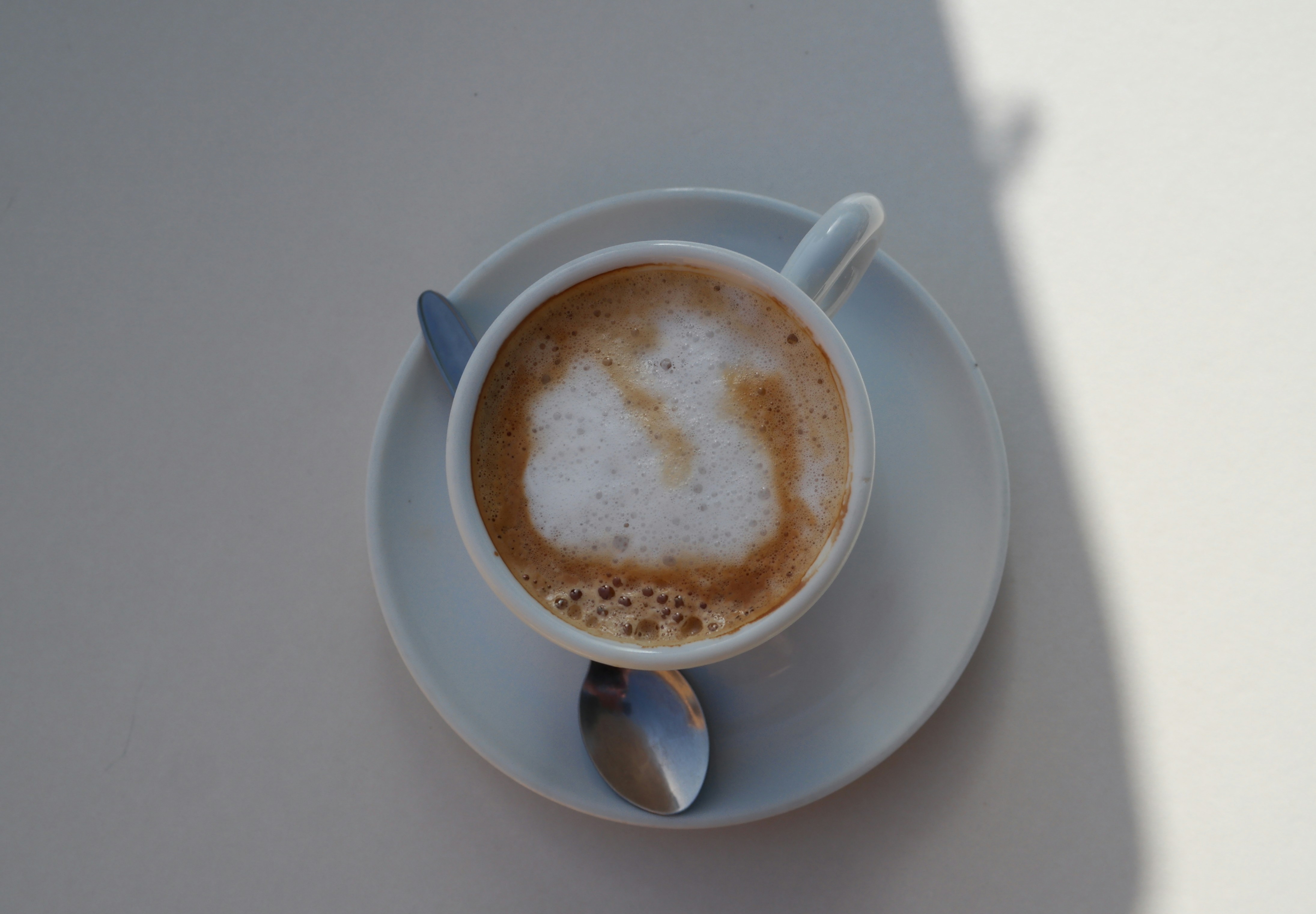 A beautifully crafted coffee cup resting on a saucer, showcasing intricate foam patterns and a spoon beside it. The soft light enhances the textures and colors.