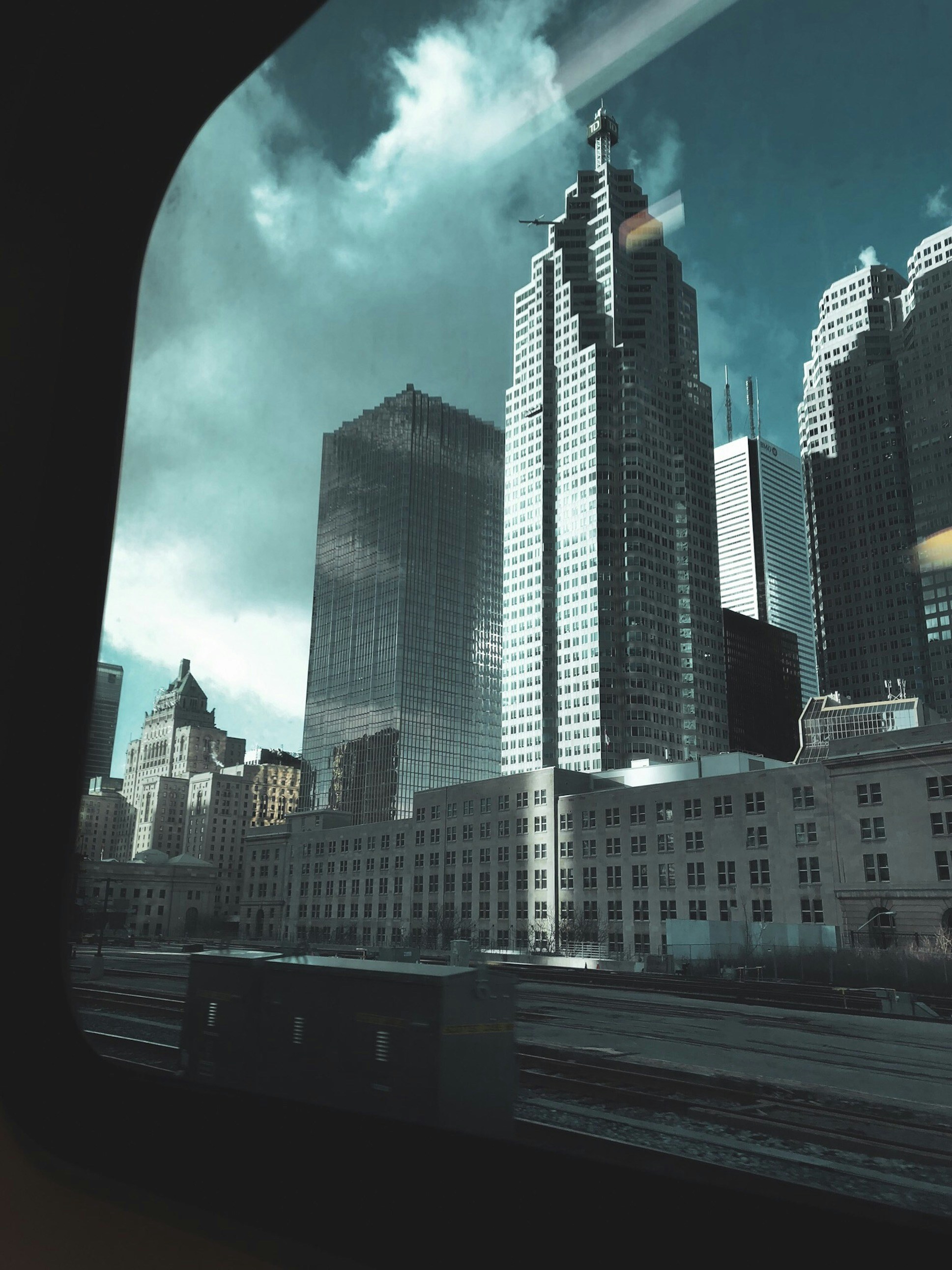 Crane-Topped Towers Framed by a Teal Skyline from a Moving Train