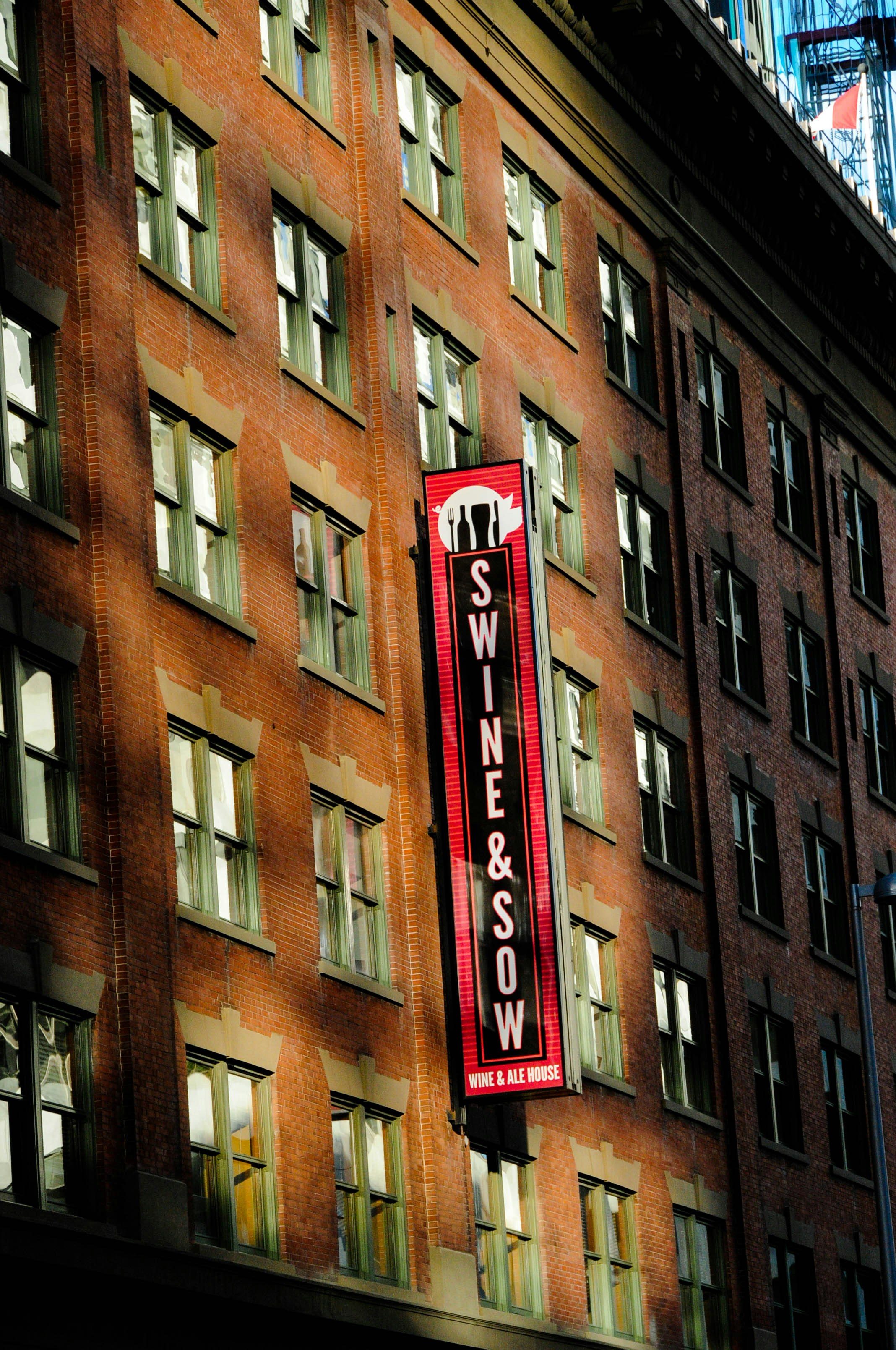 A vibrant sign for Swine & Sow, a wine and ale house, prominently displayed on a historic brick building facade.