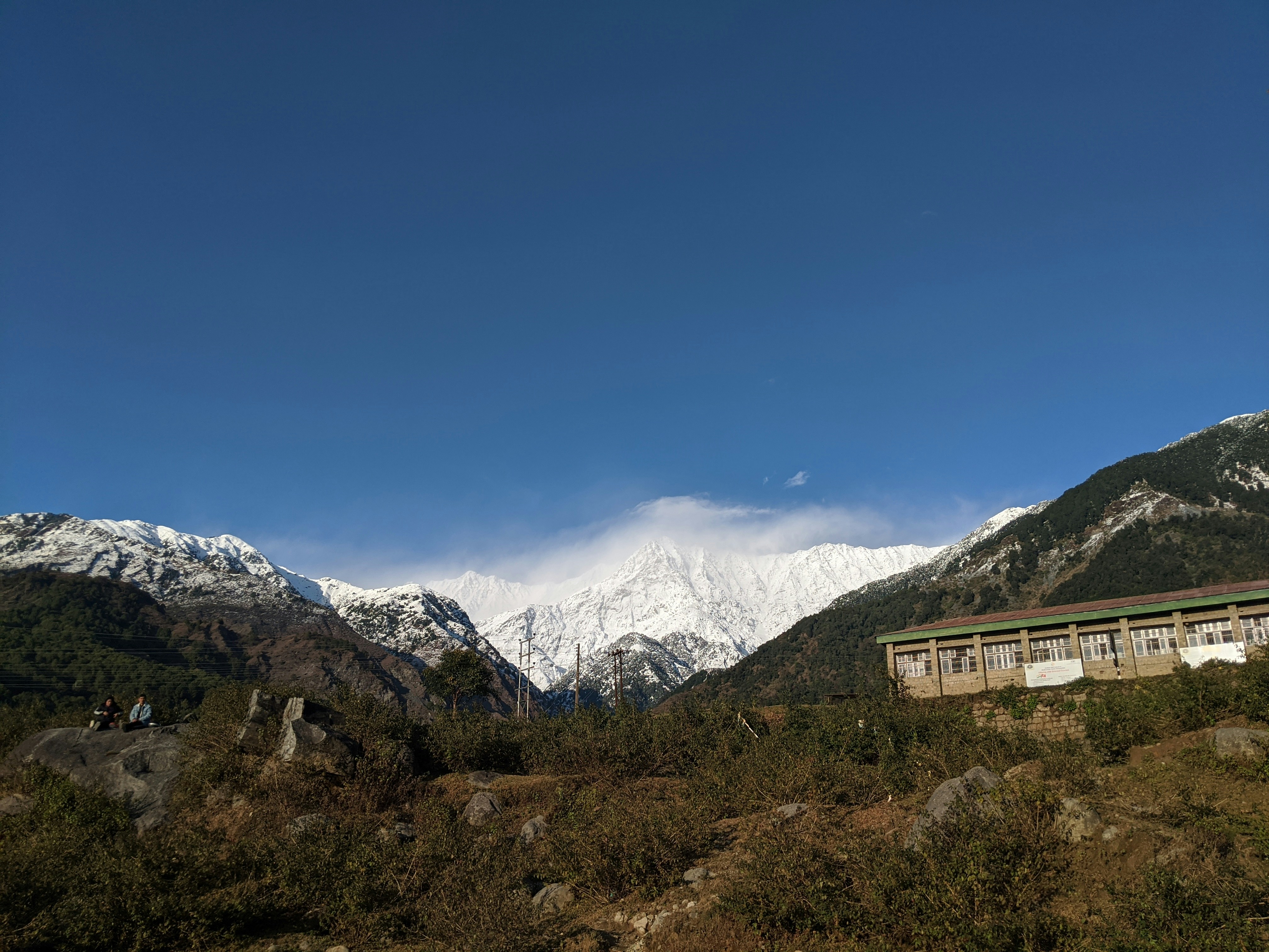 Majestic snow-covered mountains loom over a rustic building nestled in the foreground, reflecting the serene beauty of nature's grandeur.