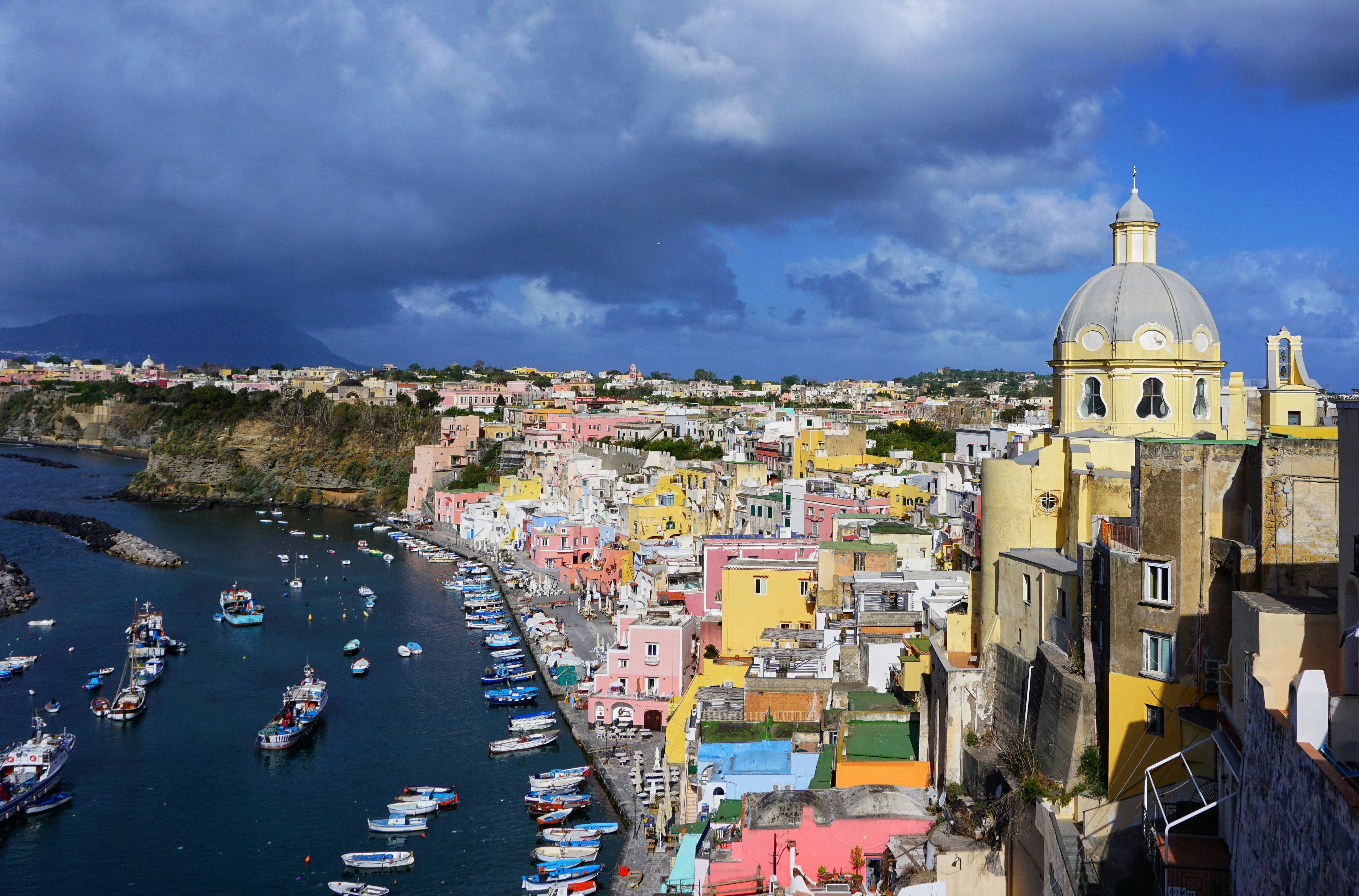 Colorful coastal town with boats lining a calm bay under a dramatic sky.