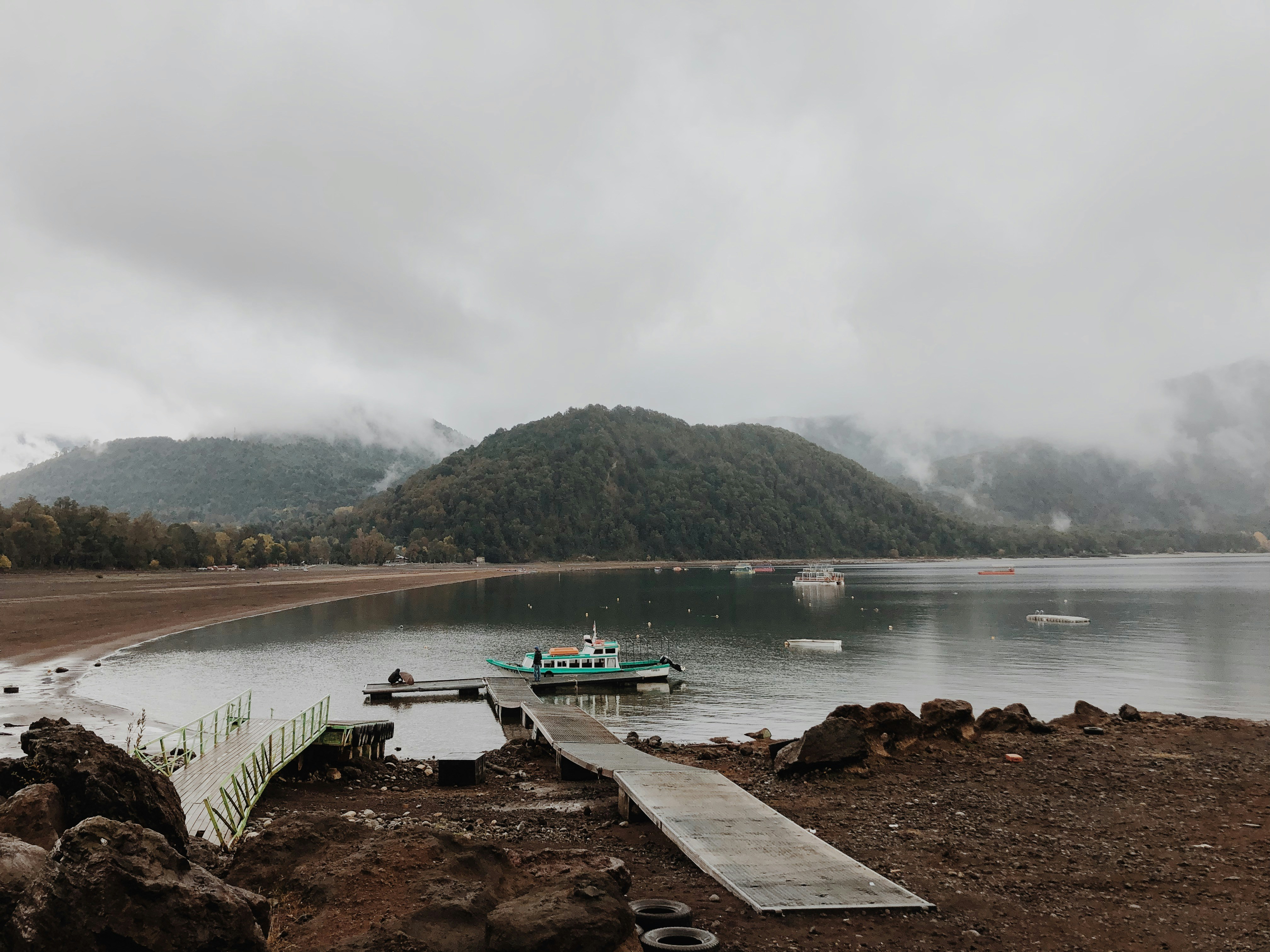 Wooden dock leading to a tranquil lake surrounded by misty hills under an overcast sky.