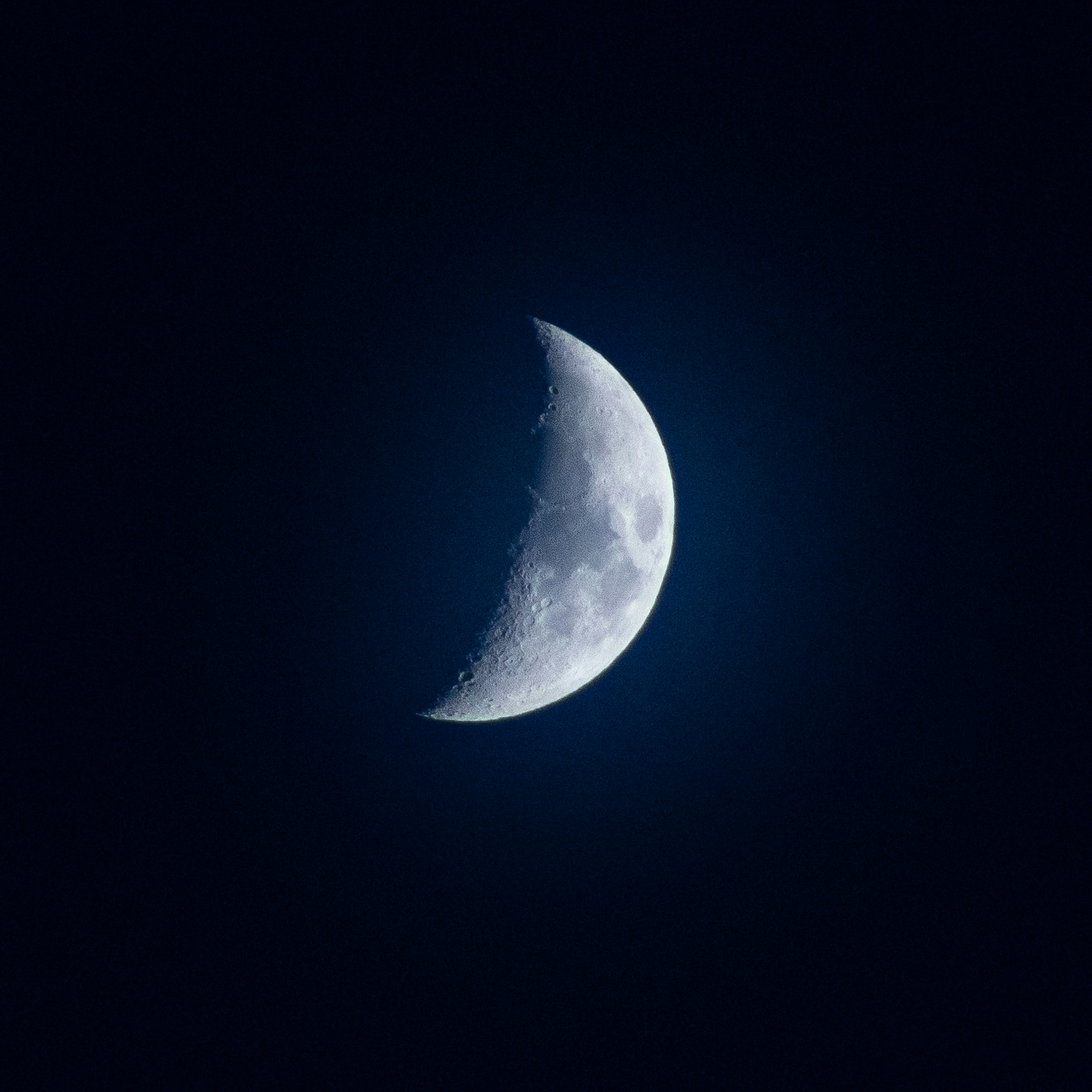 Waxing crescent moon illuminated against a deep blue sky, showcasing intricate surface details.